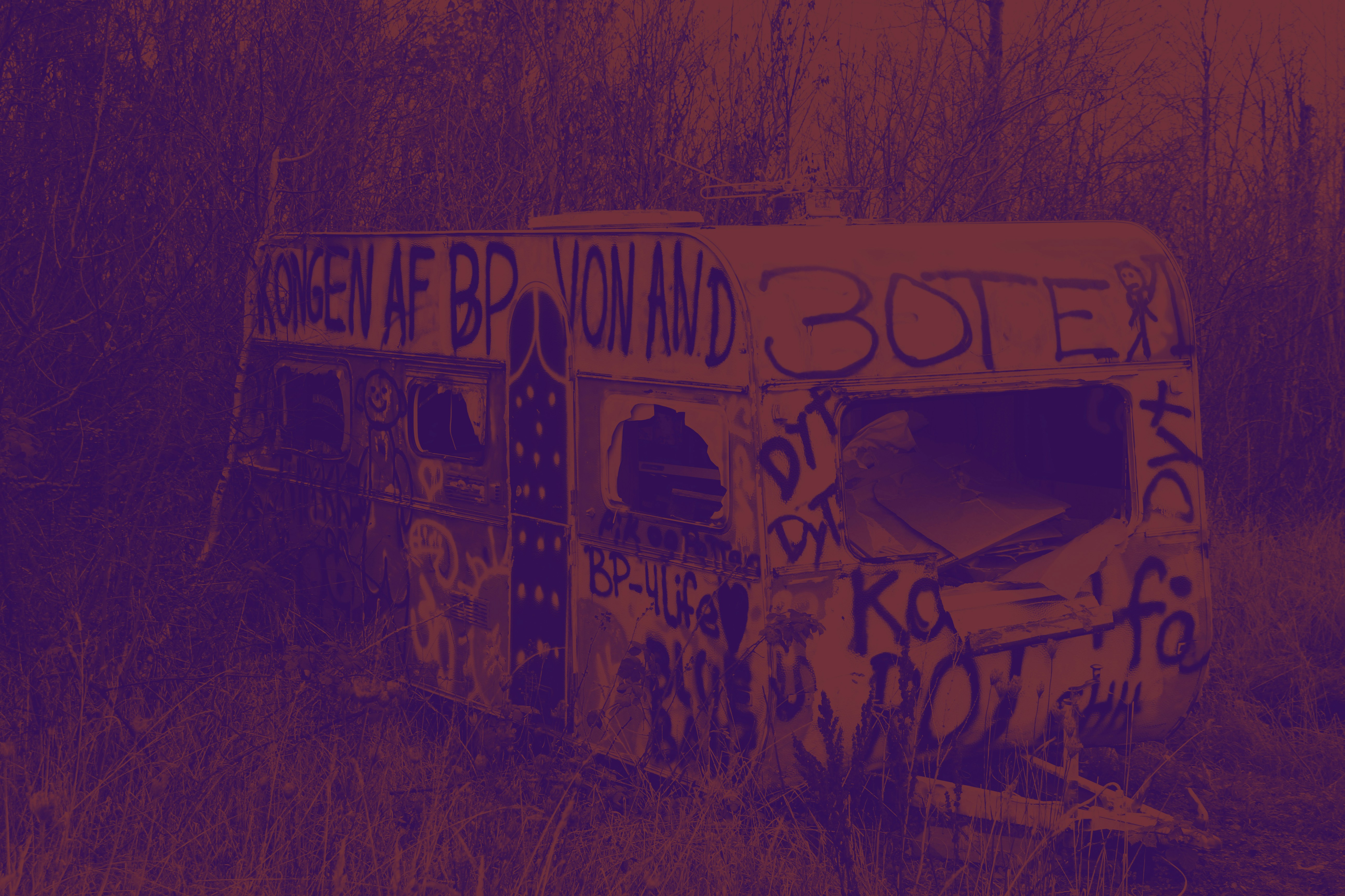 An abandoned caravan covered in vibrant graffiti, surrounded by overgrown vegetation. The scene evokes a sense of forgotten journeys.