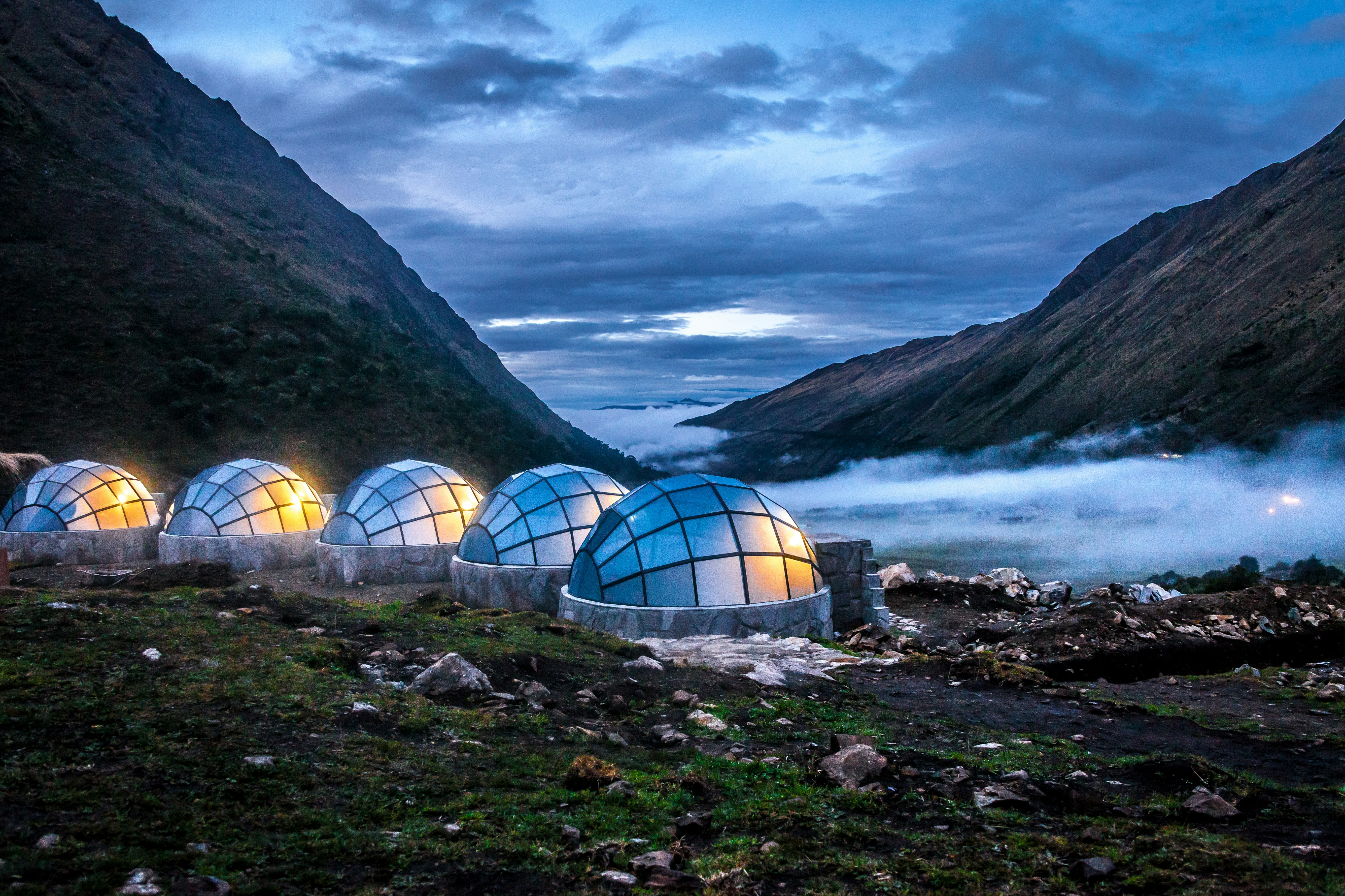 Geodesic domes glowing against a backdrop of misty Andean mountains at dusk.