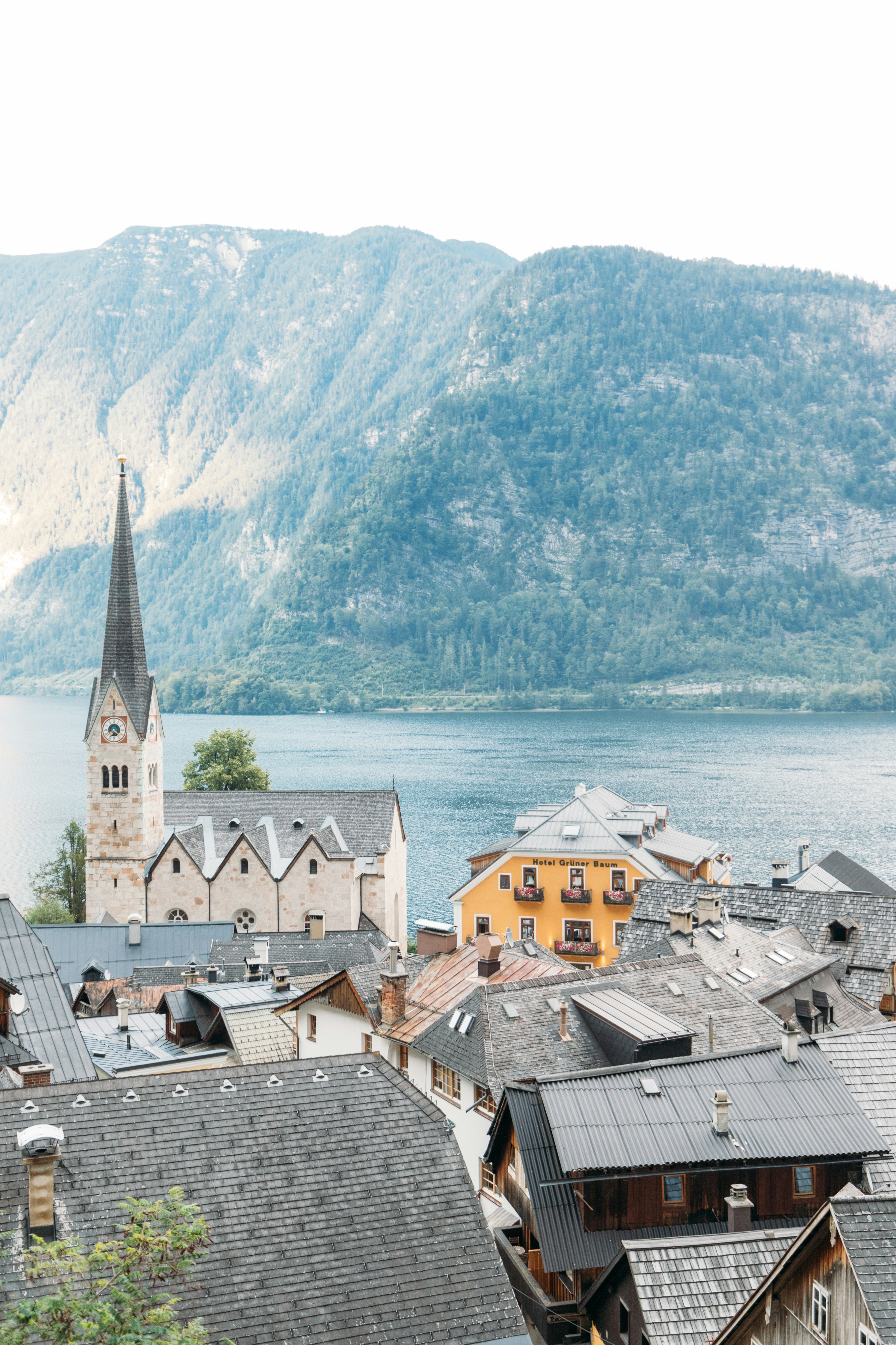 A picturesque village nestled by a tranquil lake, featuring charming architecture and a prominent church steeple against a backdrop of majestic mountains.