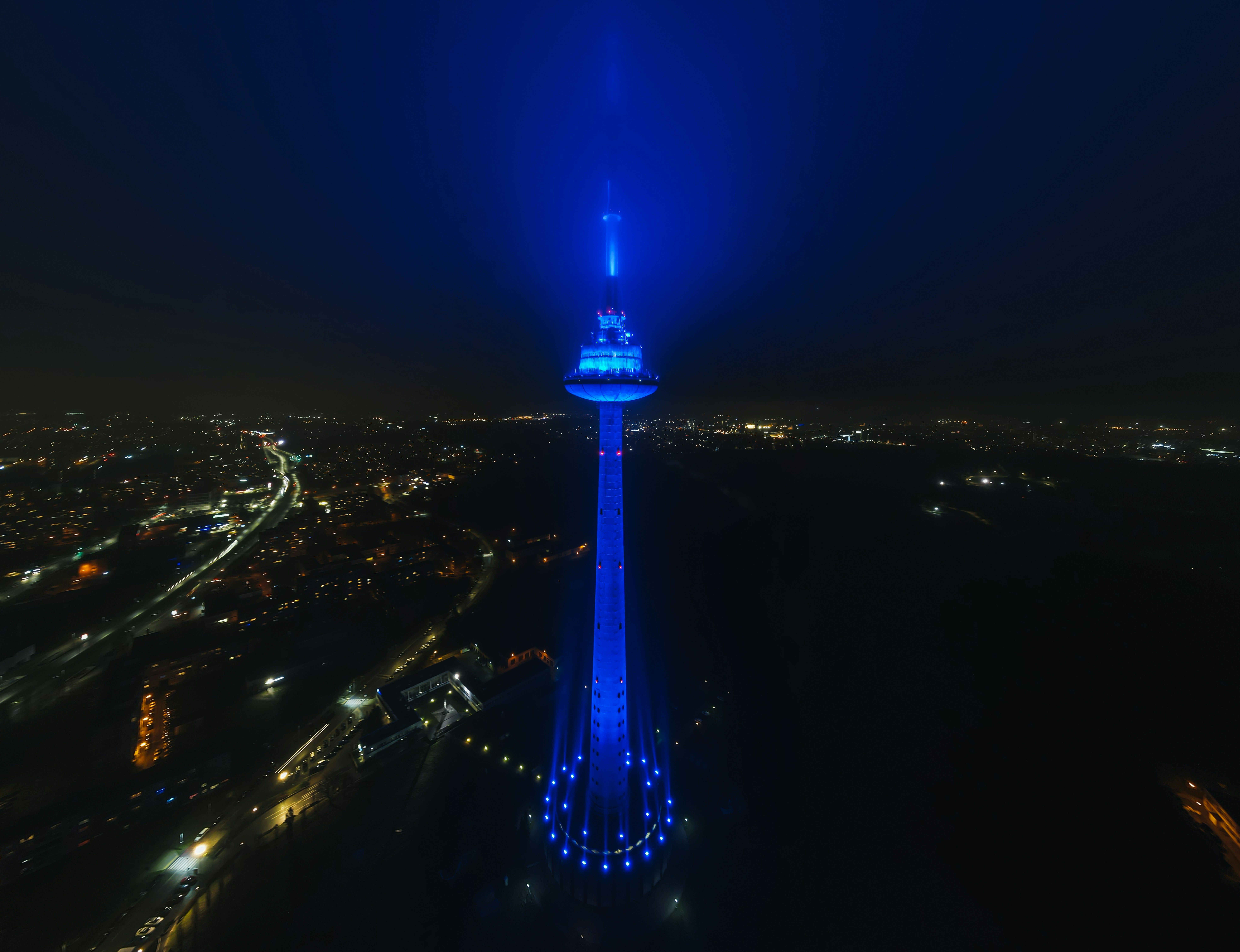 Illuminated tower glowing blue against a sprawling cityscape at night.