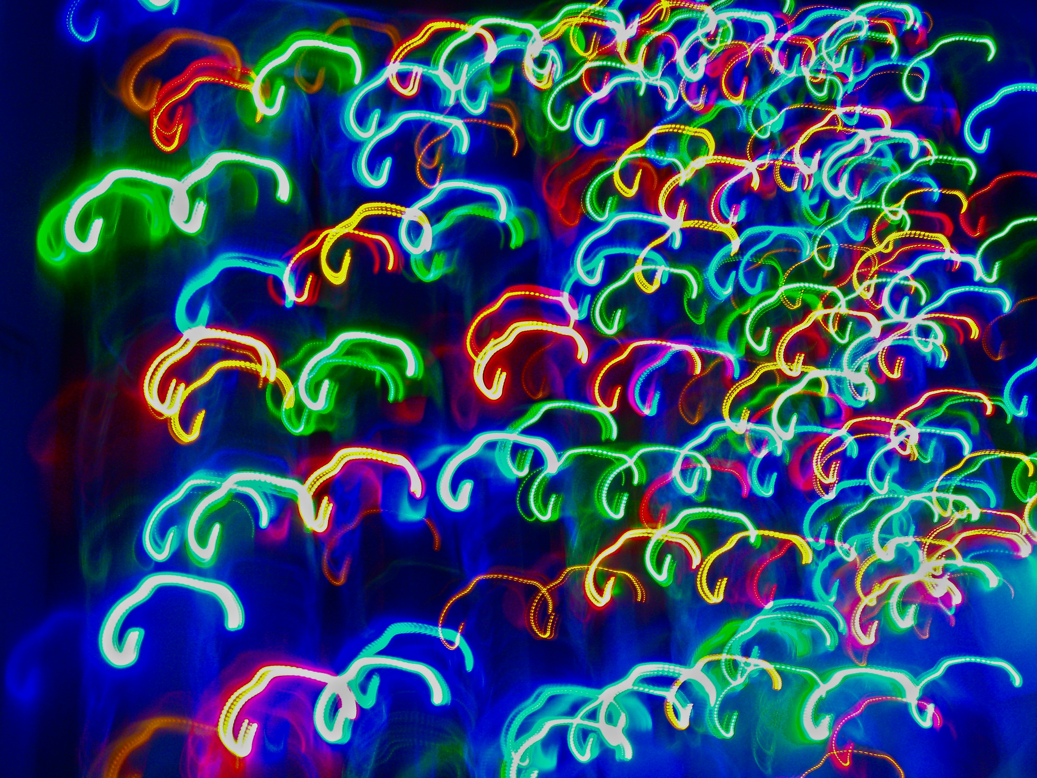 Long-exposure photograph capturing colorful neon light trails forming looping curves. The abstract composition emphasizes motion and color over a discernible subject.