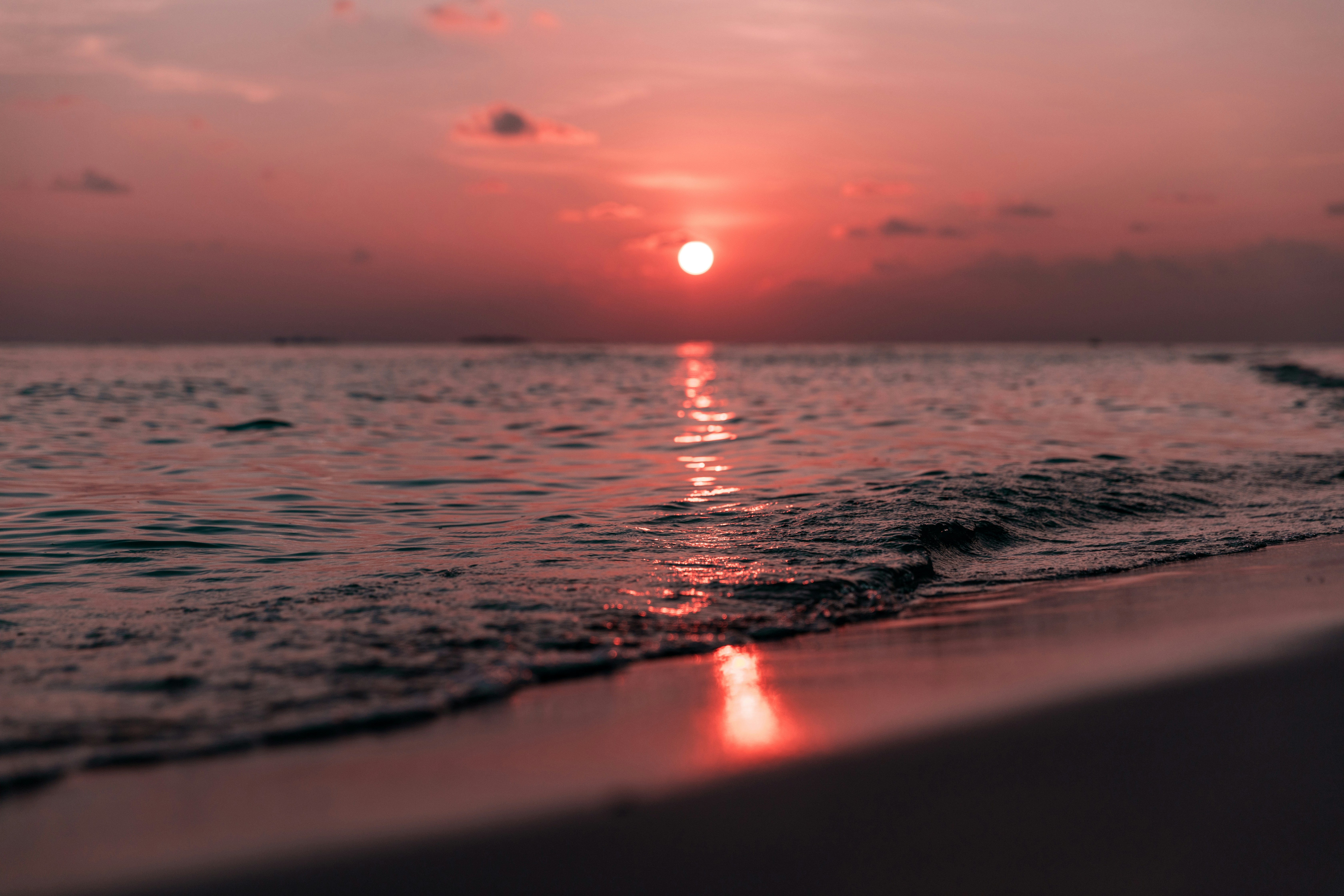 Sunset casting a warm glow over gentle ocean waves and sandy shoreline.