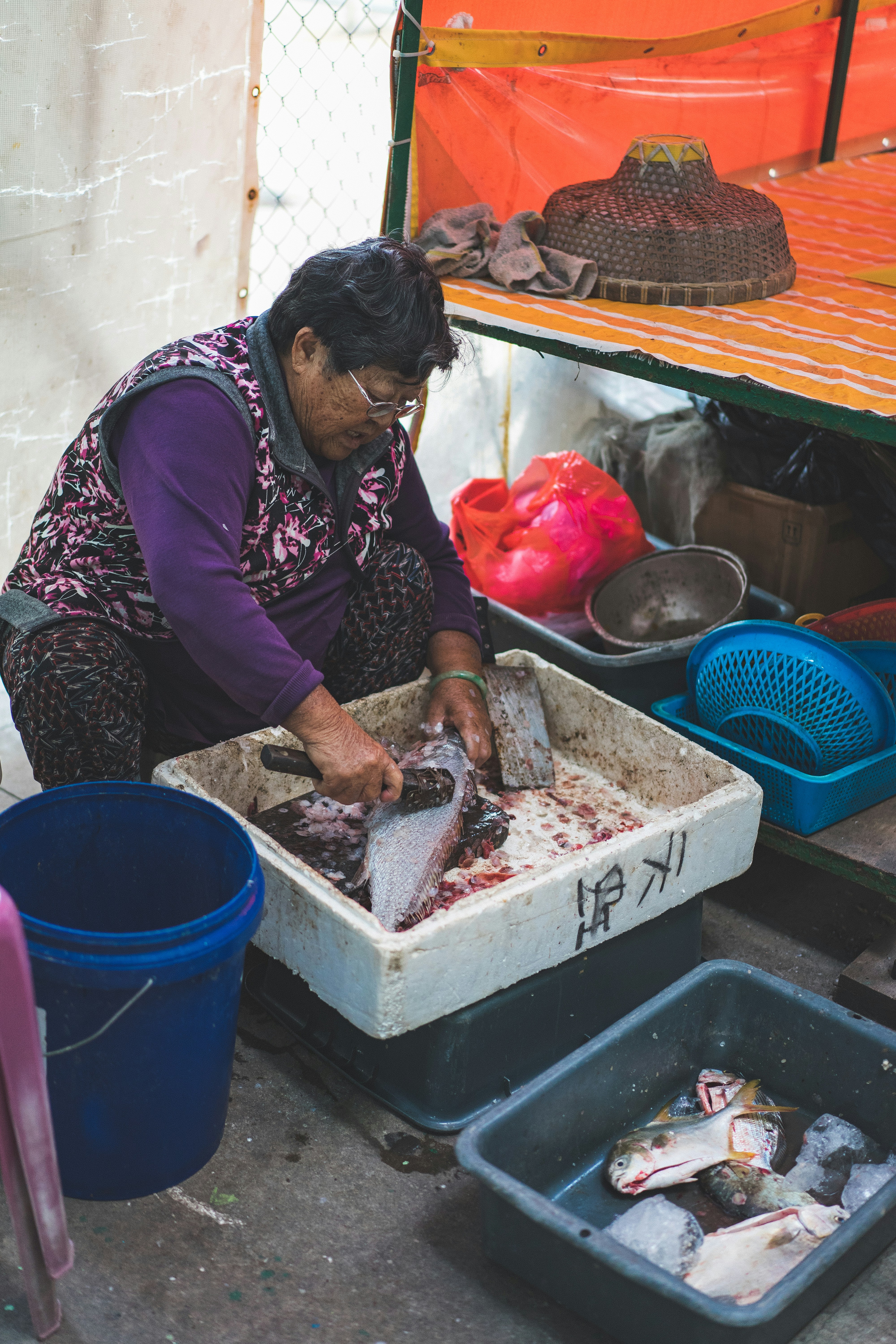 A vendor skillfully filleting fish in a bustling market, surrounded by colorful containers and vibrant textiles.