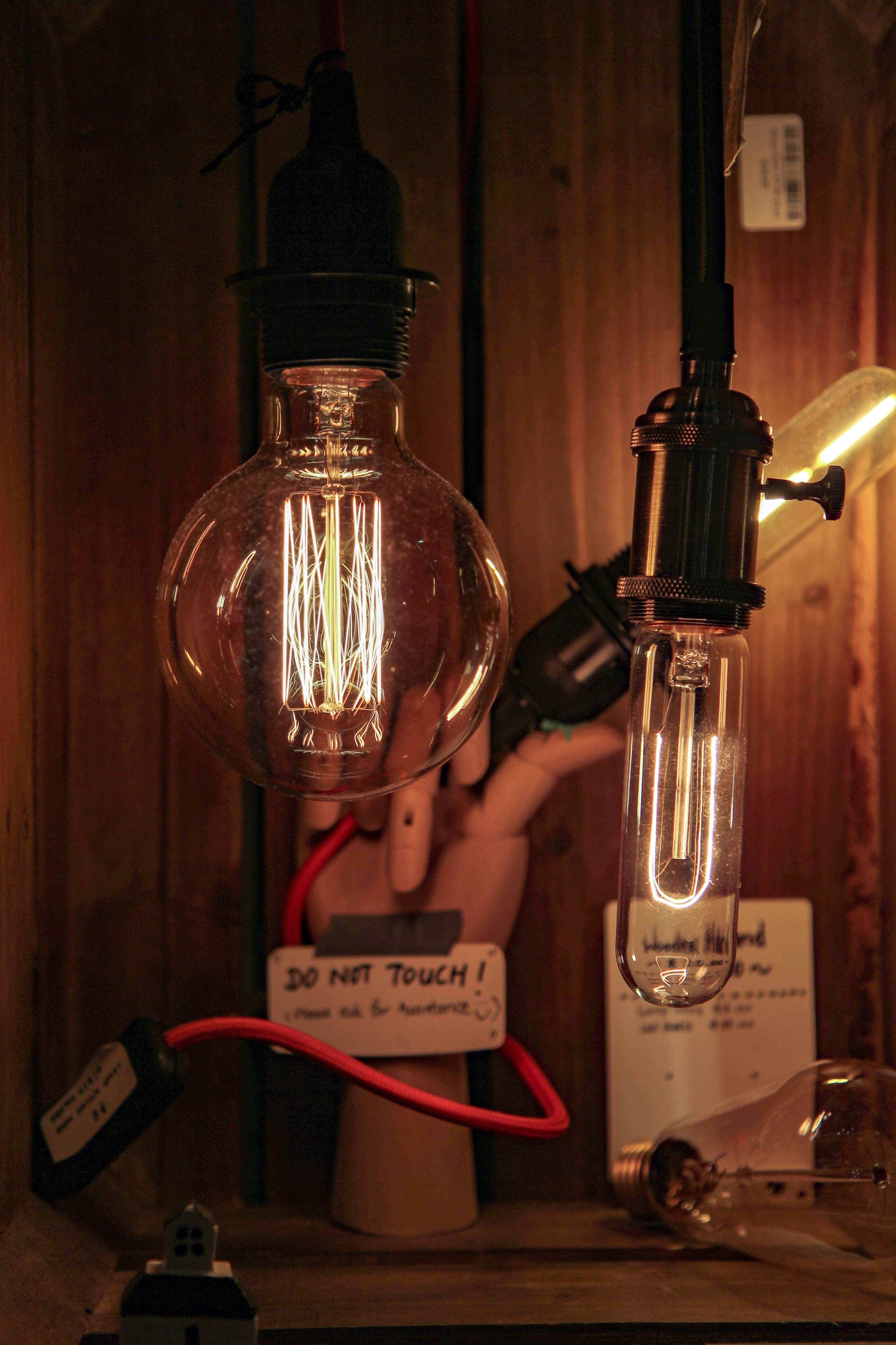 Edison-style bulbs glowing warmly against a wooden backdrop, with a mannequin hand holding one bulb.