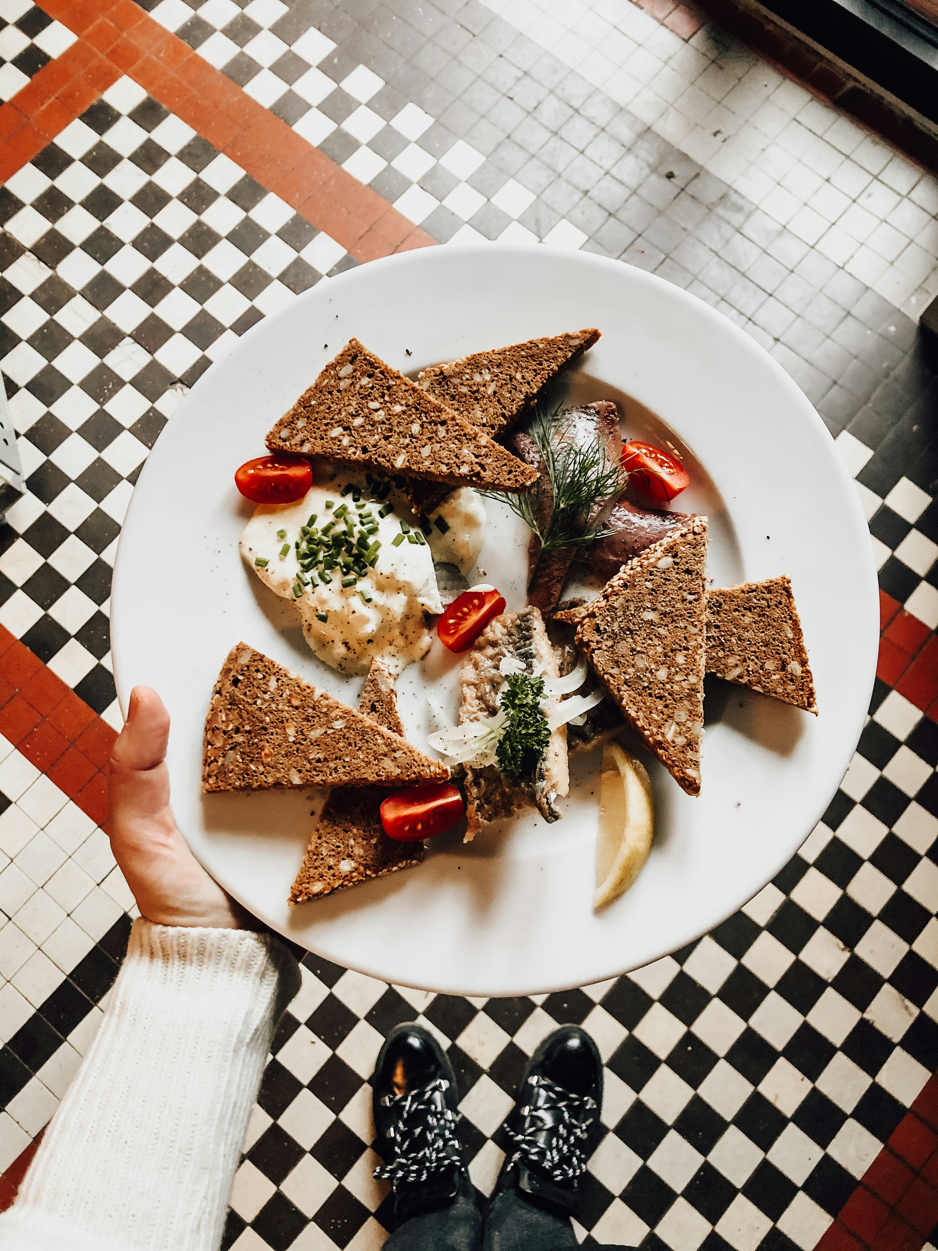 A beautifully arranged plate featuring dark bread triangles, fresh herbs, and colorful garnishes, set against a patterned floor.