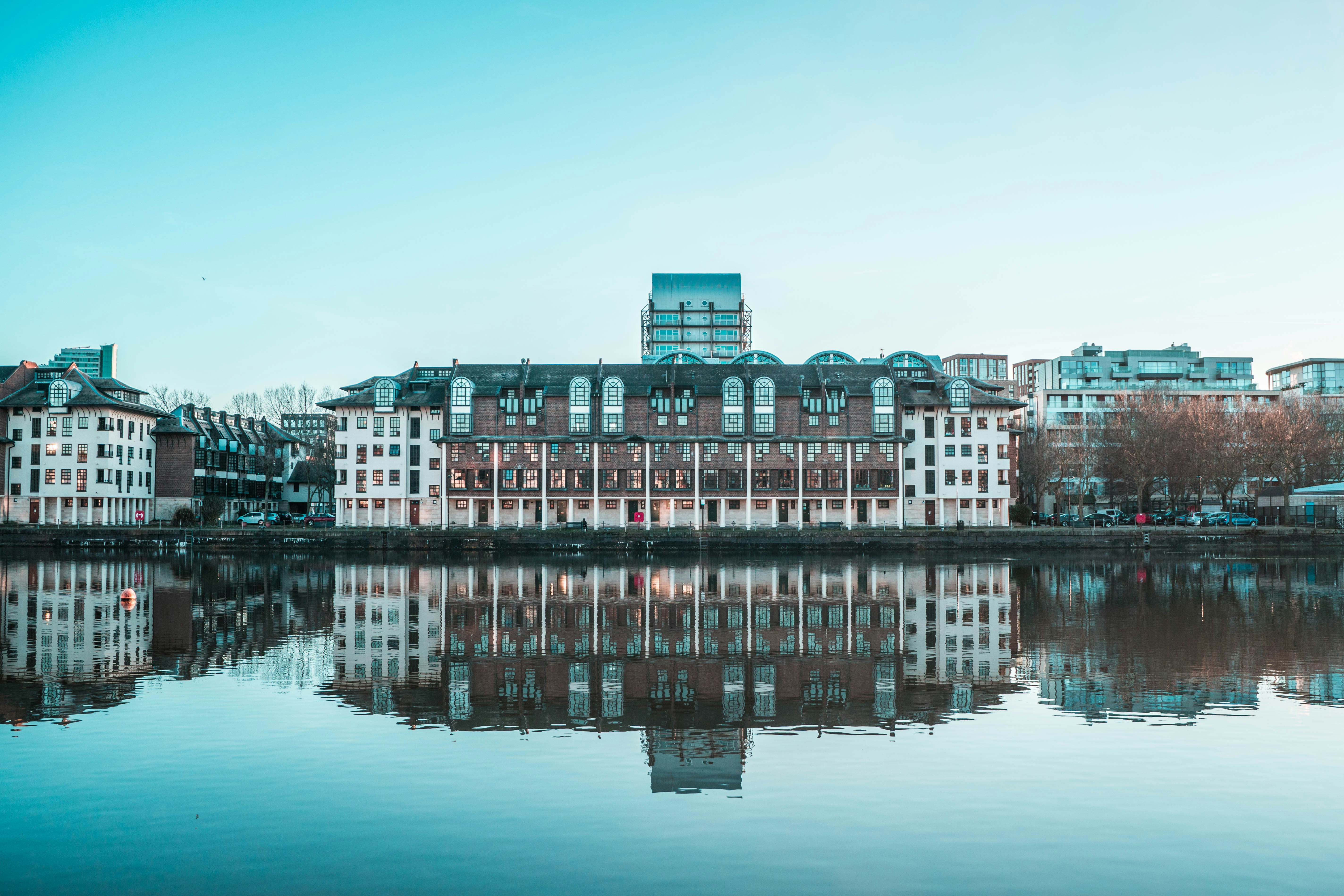 Cityscape mirrored in a calm river under a clear blue sky.