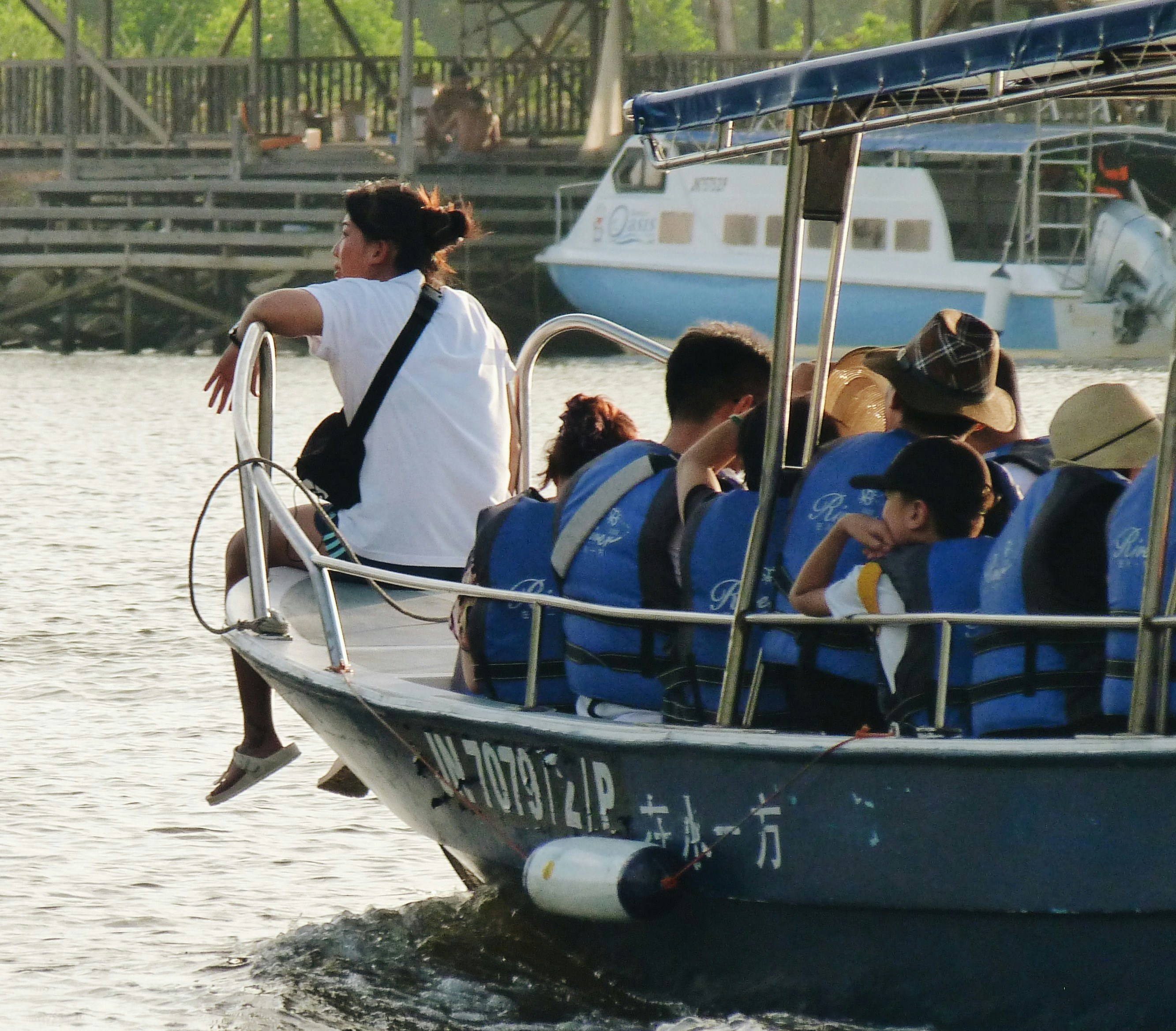 A group of people enjoying a boat ride, with one person casually seated on the edge, overlooking the water. The scene captures a relaxed atmosphere under the sun.