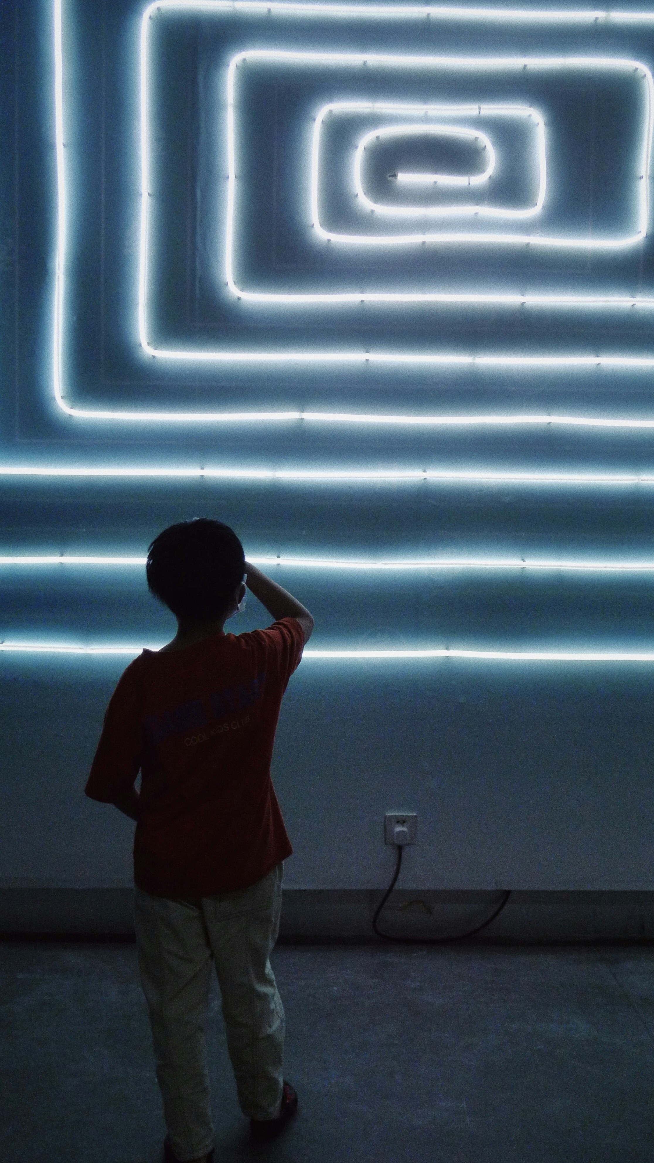 Child observing a series of glowing, concentric light patterns on a wall, evoking a sense of wonder and exploration.