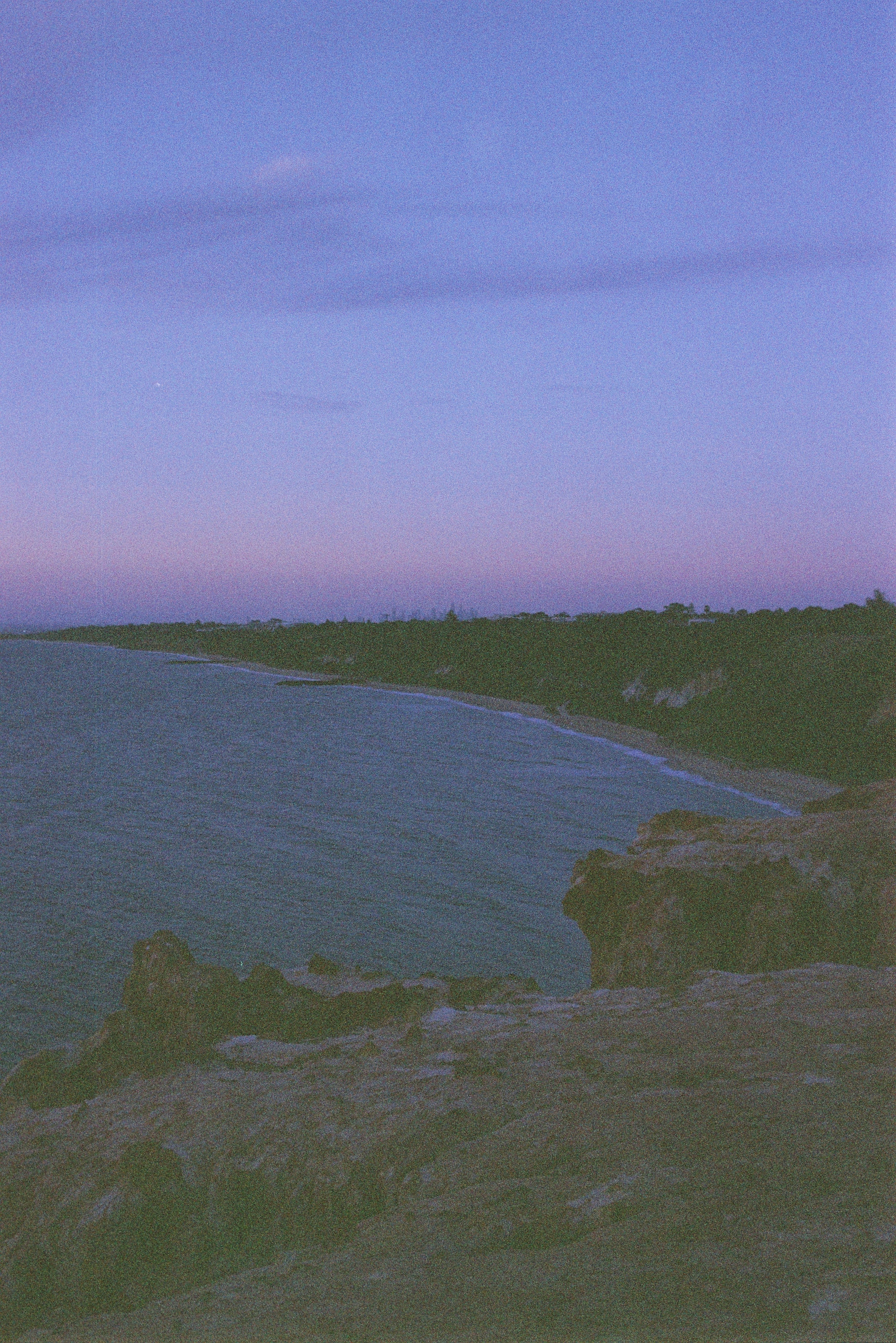 Serene coastal landscape at twilight, showcasing a gentle curve of the shore and the transition of colors in the sky.