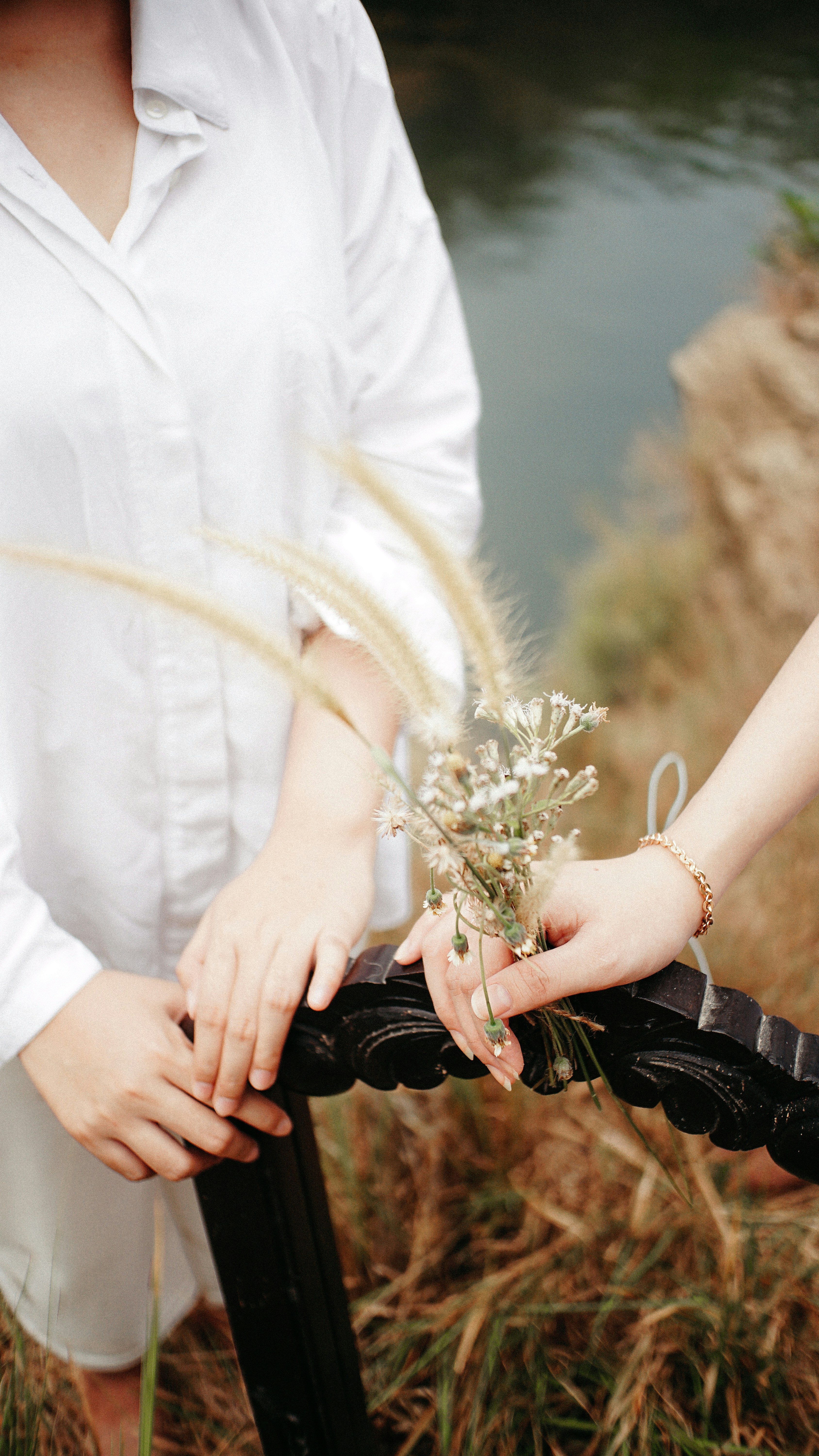 Riverbank Reverie: Hands, Wildflowers, and an Ornate Railing