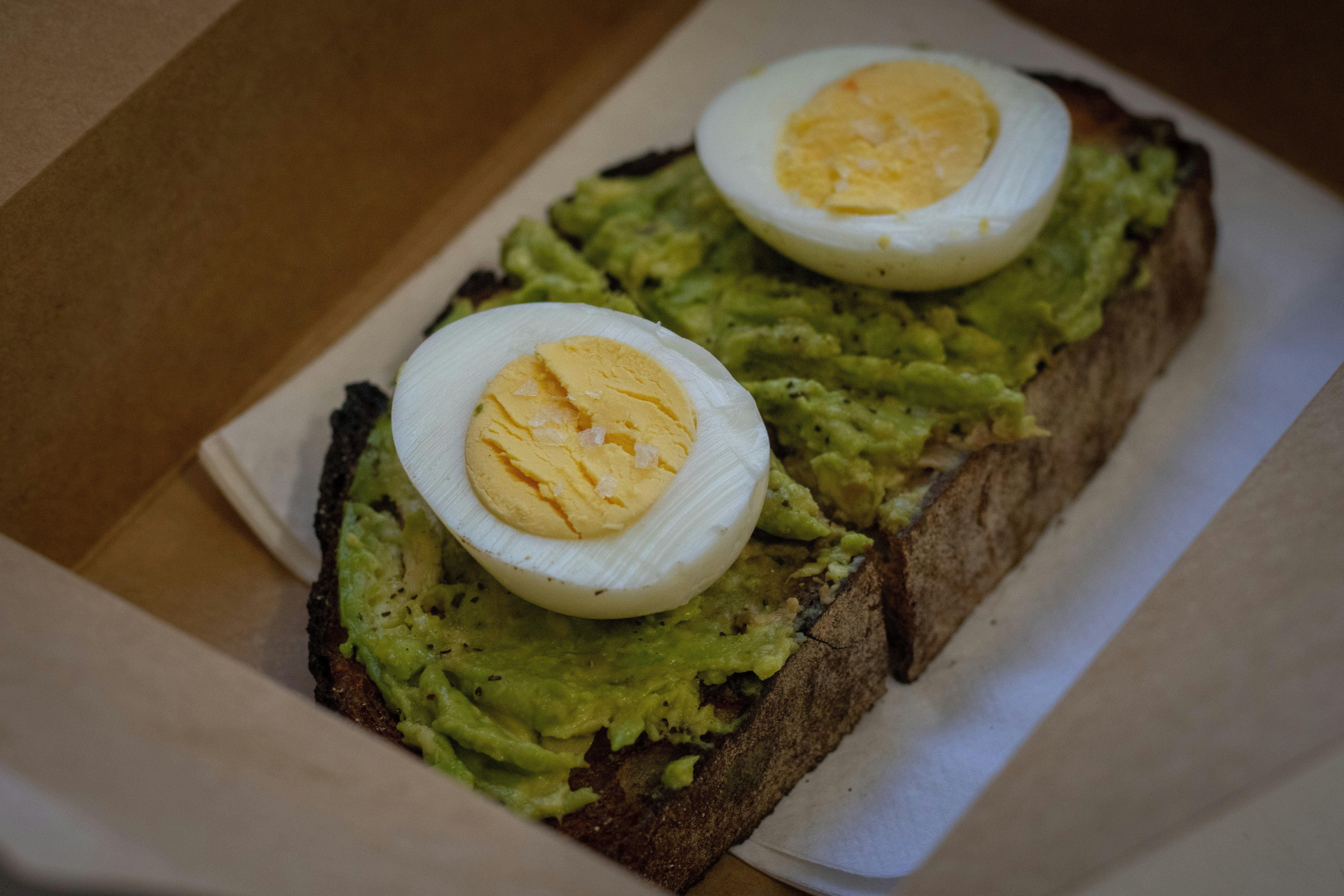 Avocado-Spread Toast with Halved Boiled Eggs in a Cardboard Box