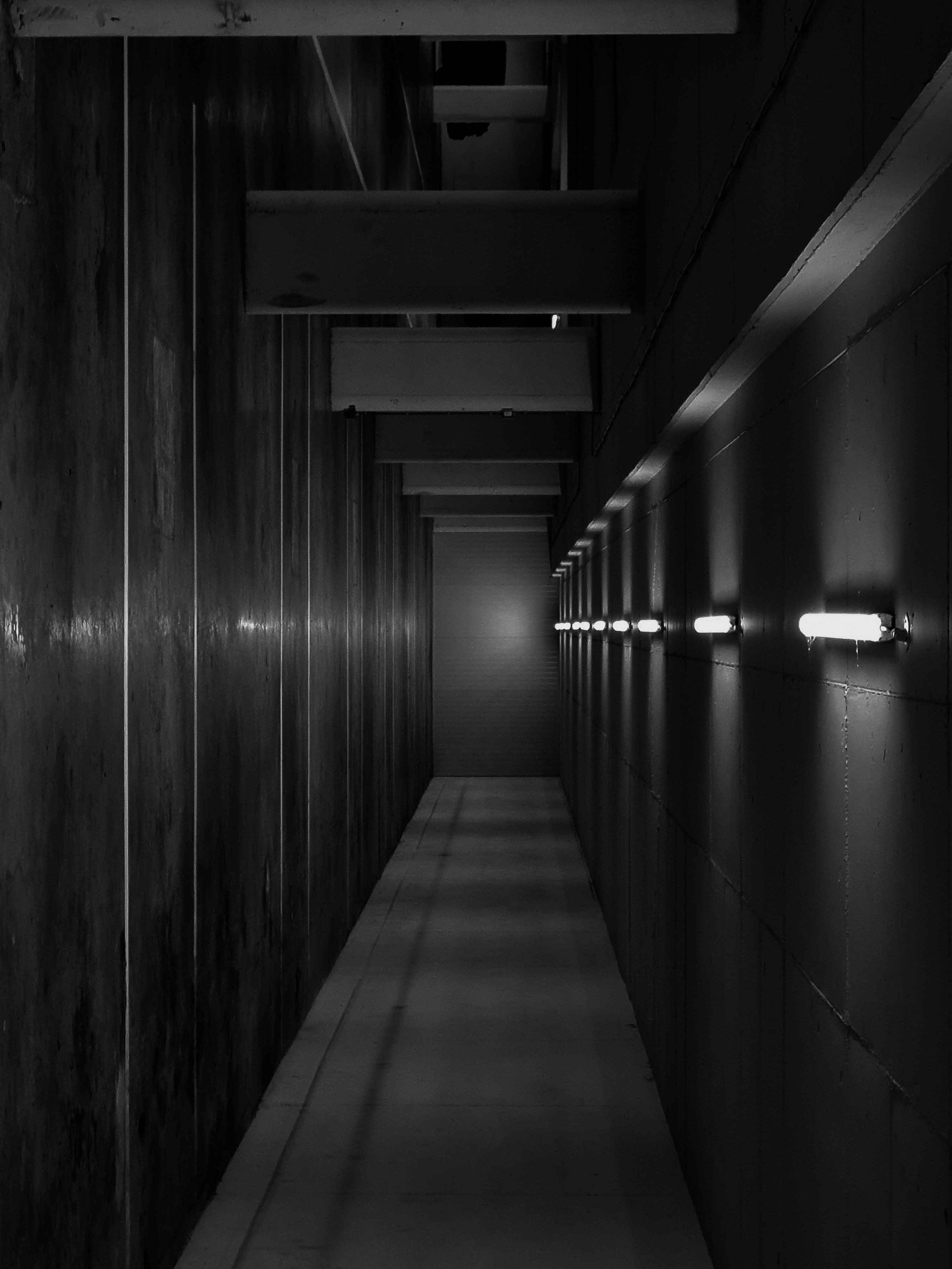 A dimly lit corridor with concrete walls and overhead lights guiding the way forward.