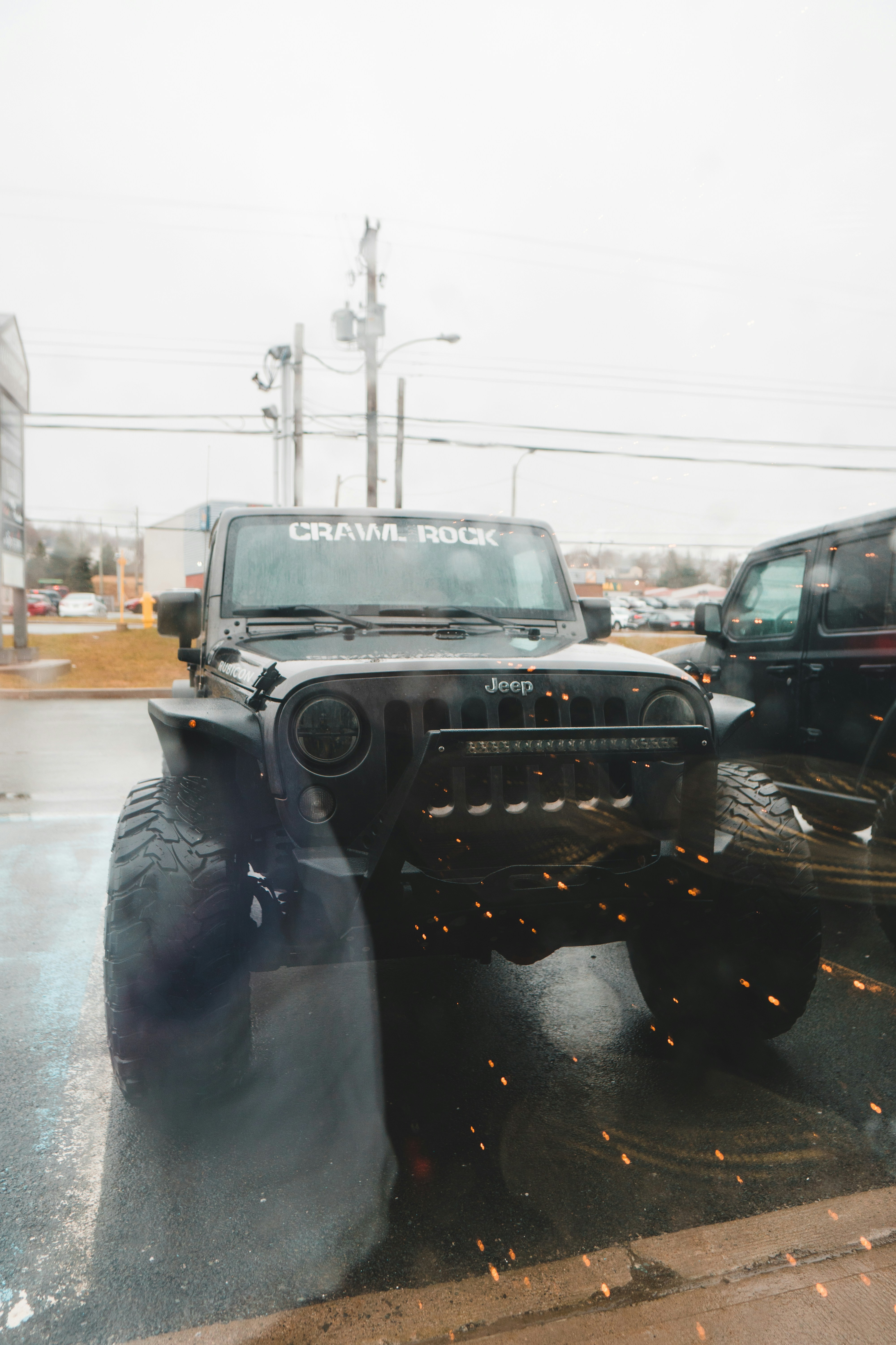 Black Jeep Wrangler parked prominently, showcasing its rugged exterior and off-road capabilities, with a blurred urban backdrop. 