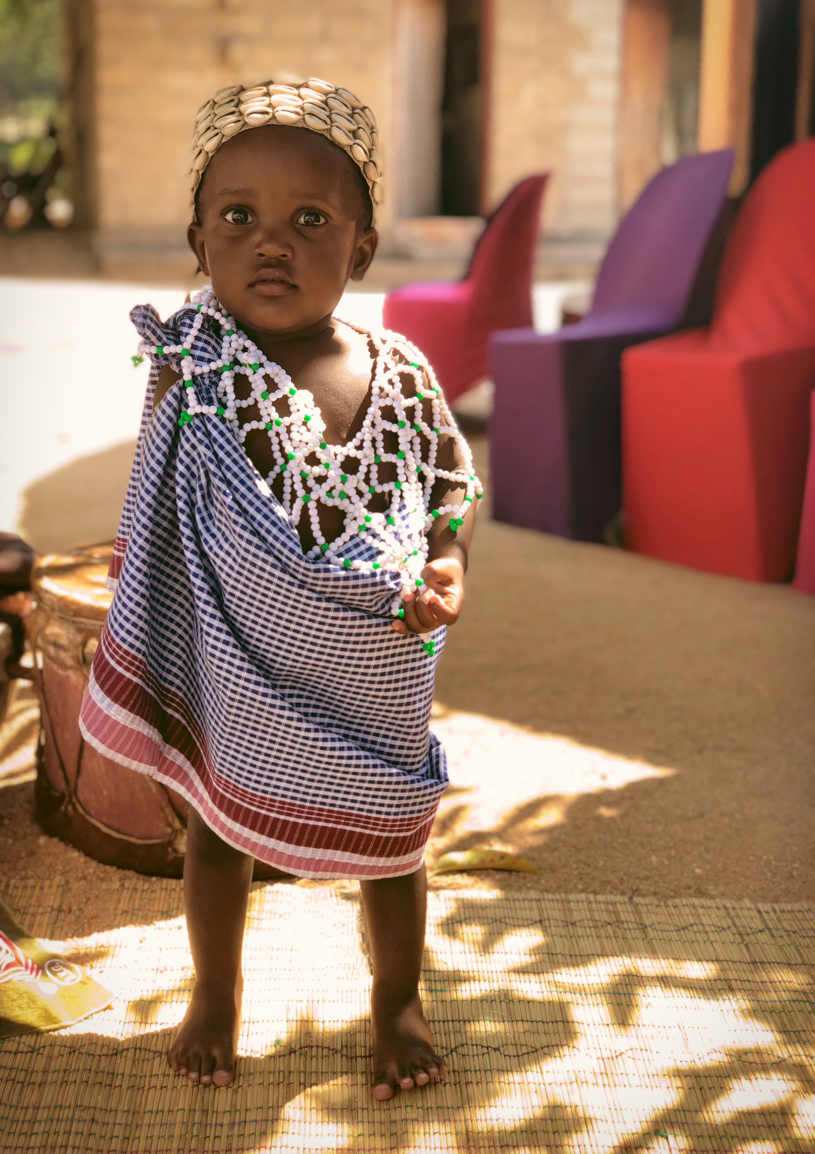 Beaded Grace in Warm Light: A Young Child Amid Colorful Porch Furniture
