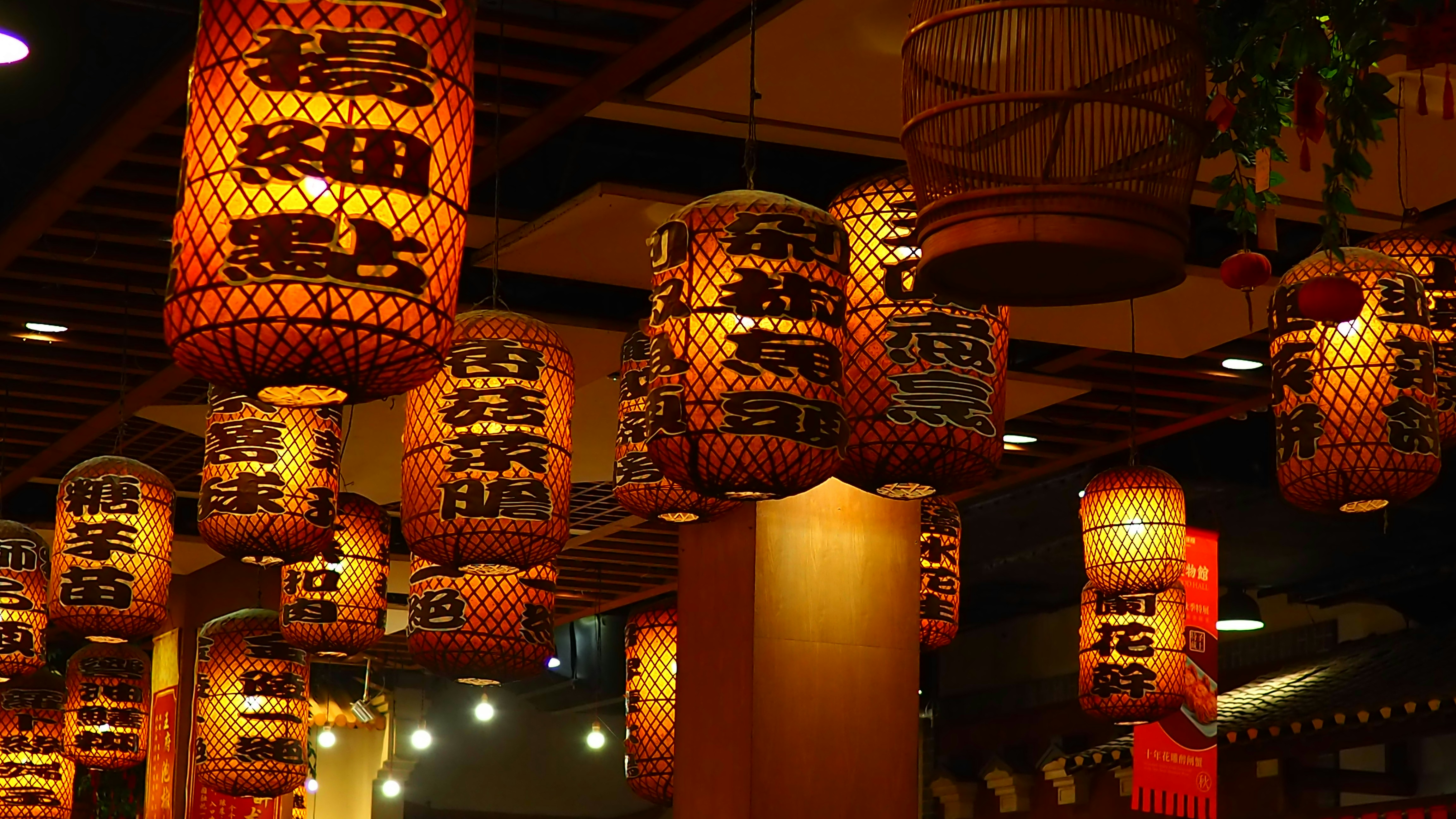 A collection of vibrant lanterns adorned with intricate characters, casting a warm glow in a bustling interior space.