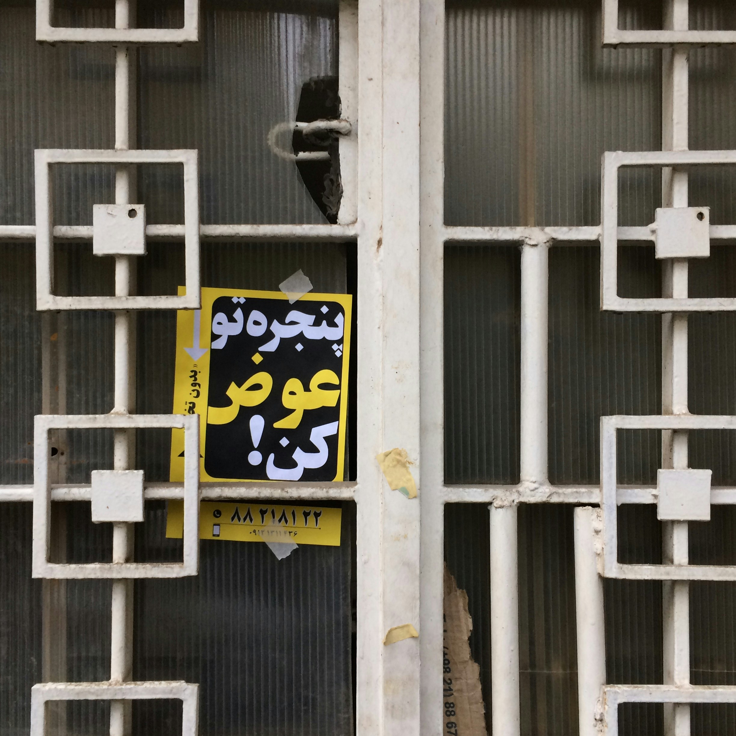 Yellow Persian Script Sticker on a Weathered Gate Framed by Gridded Glass