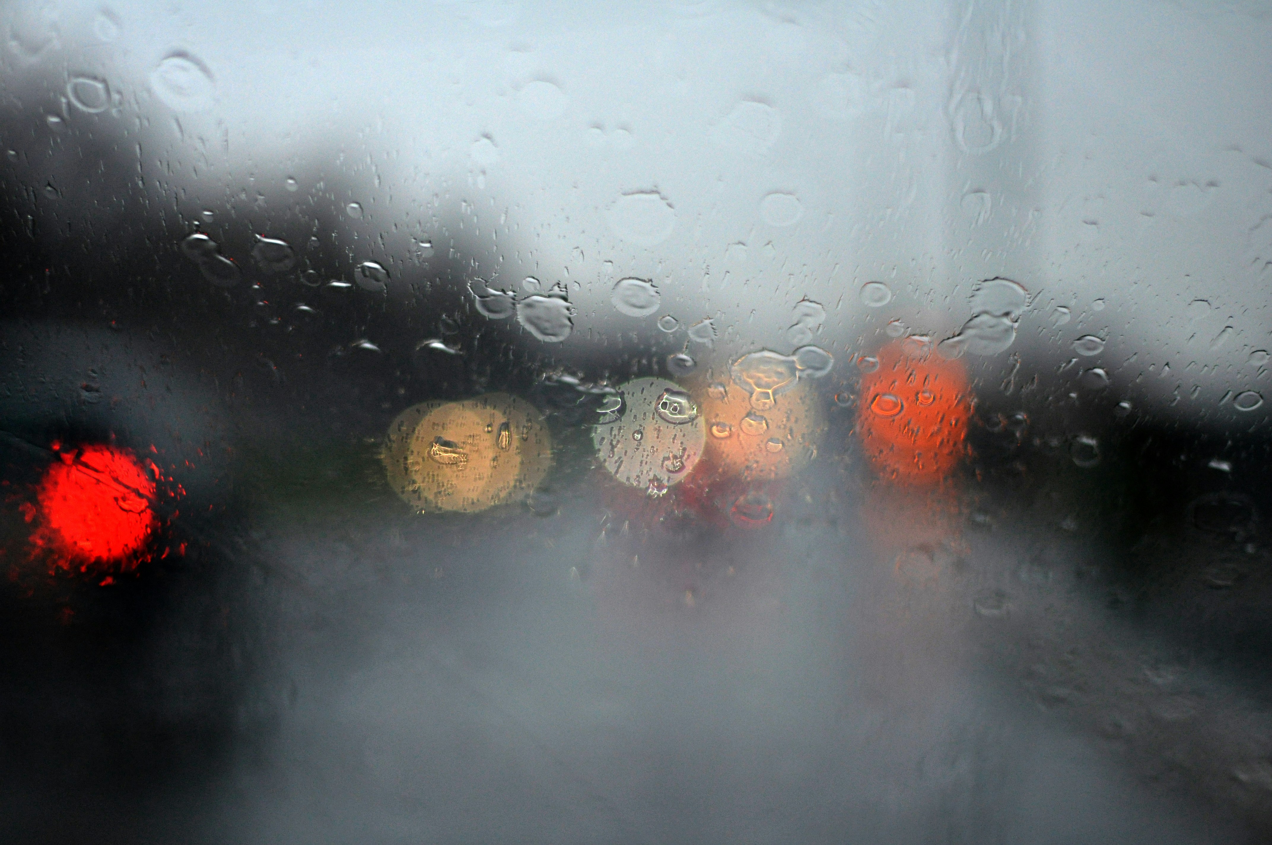 Blurry lights of vehicles seen through a rain-soaked window, creating a dynamic urban atmosphere.