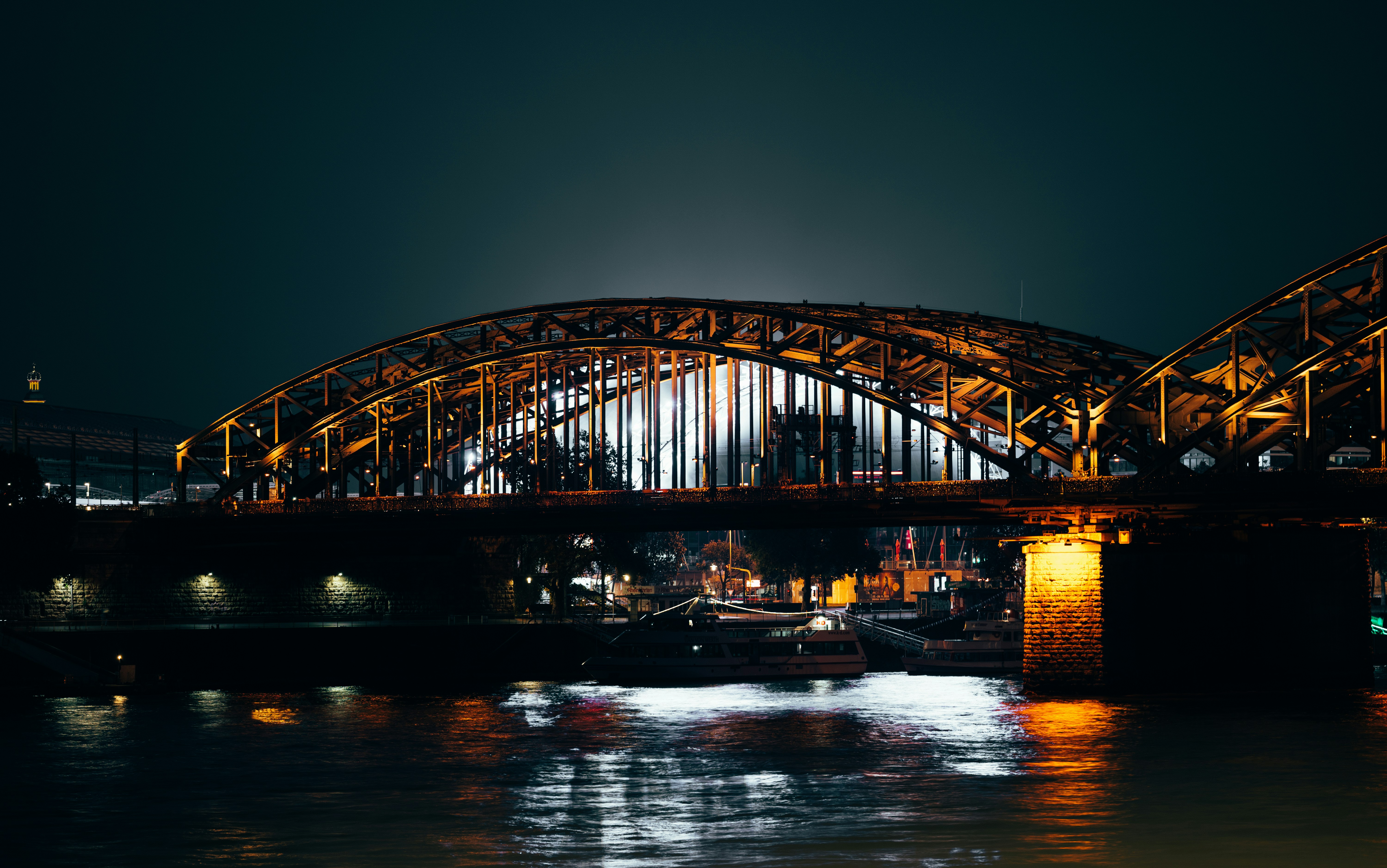 A beautifully illuminated bridge arches over a calm river at night, showcasing intricate architectural details against a dark sky.