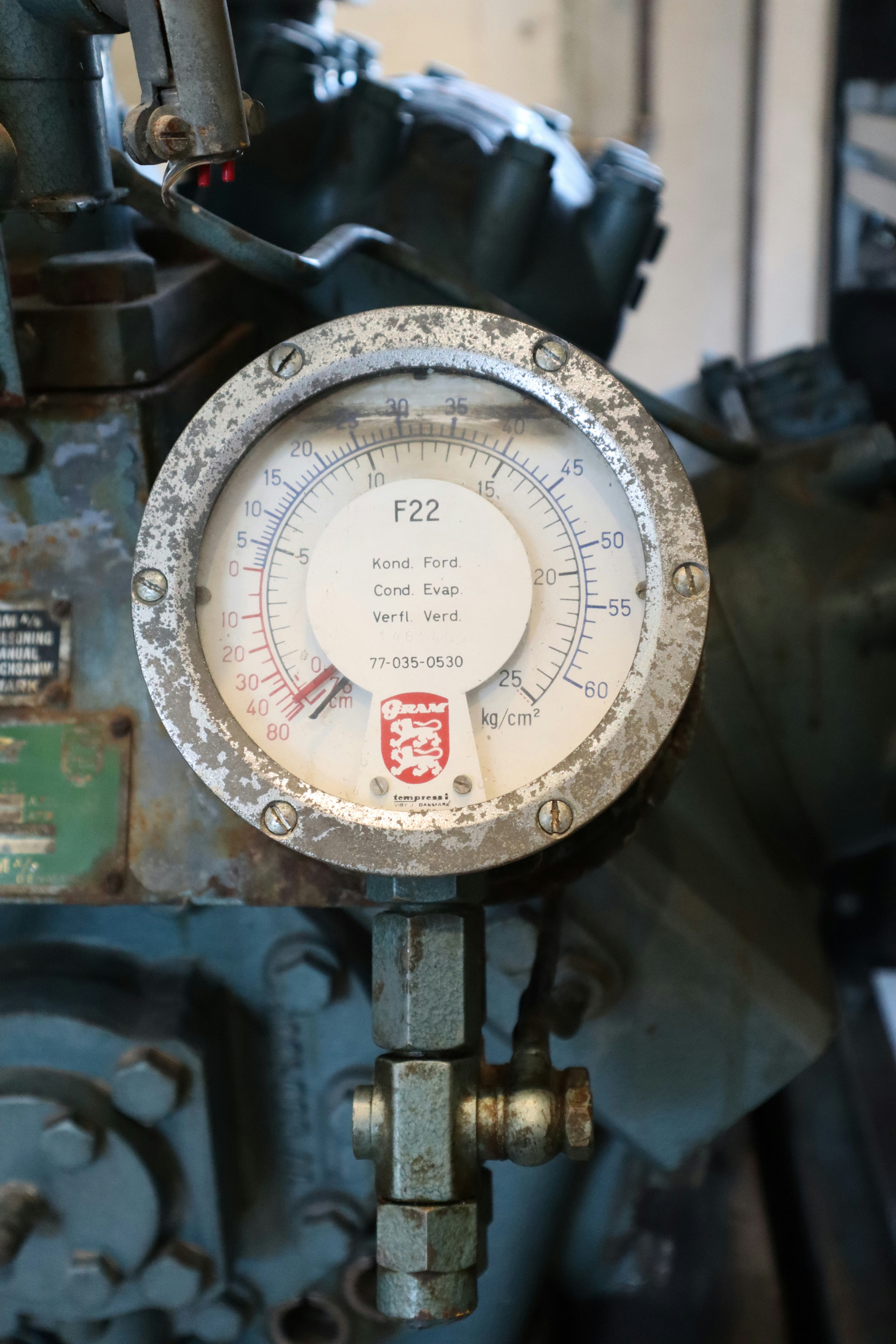 Engineered Gauge: A Weathered Pressure Dial Amid Industrial Machinery
