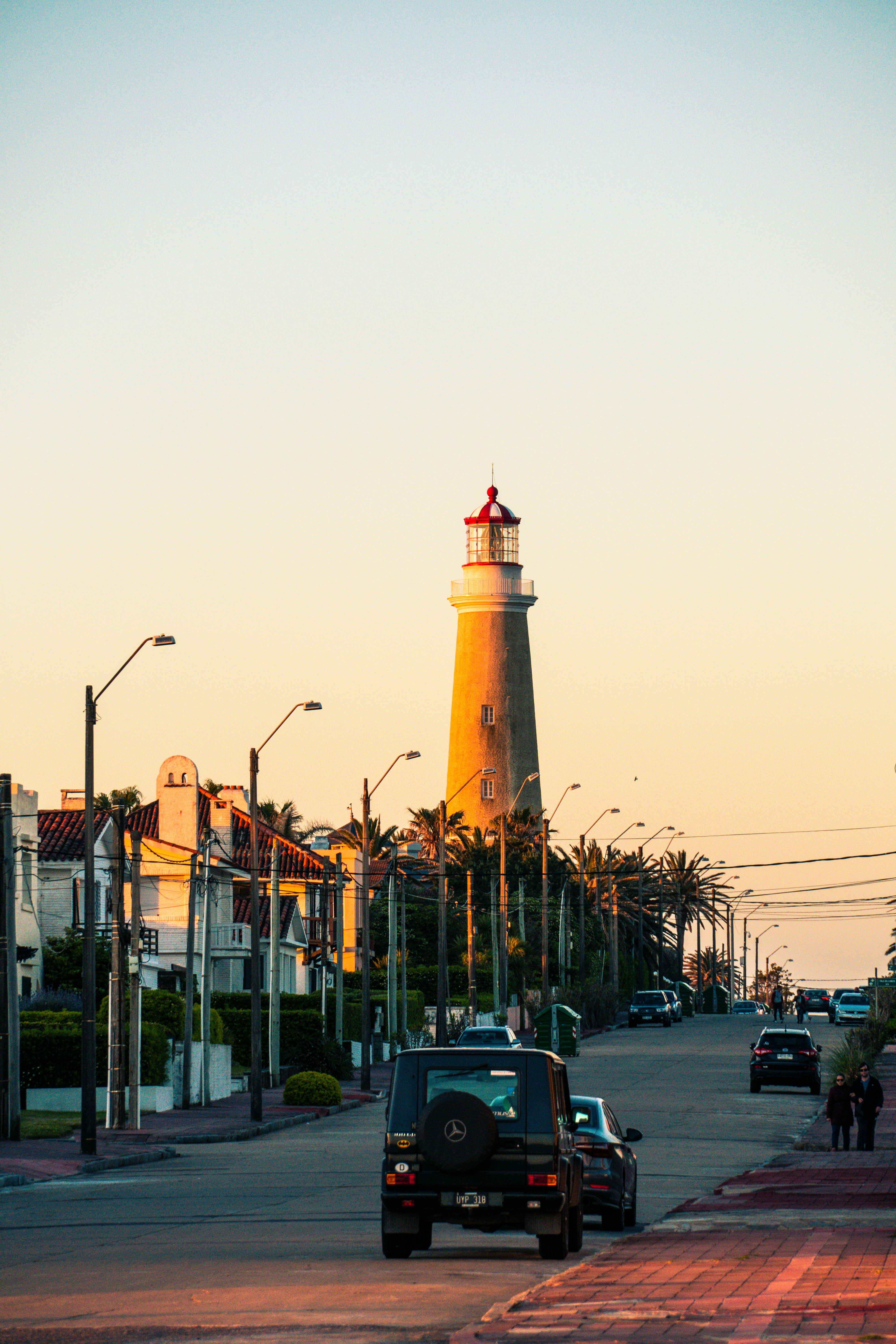 Historic lighthouse standing tall at dusk, surrounded by palm trees and charming coastal architecture.