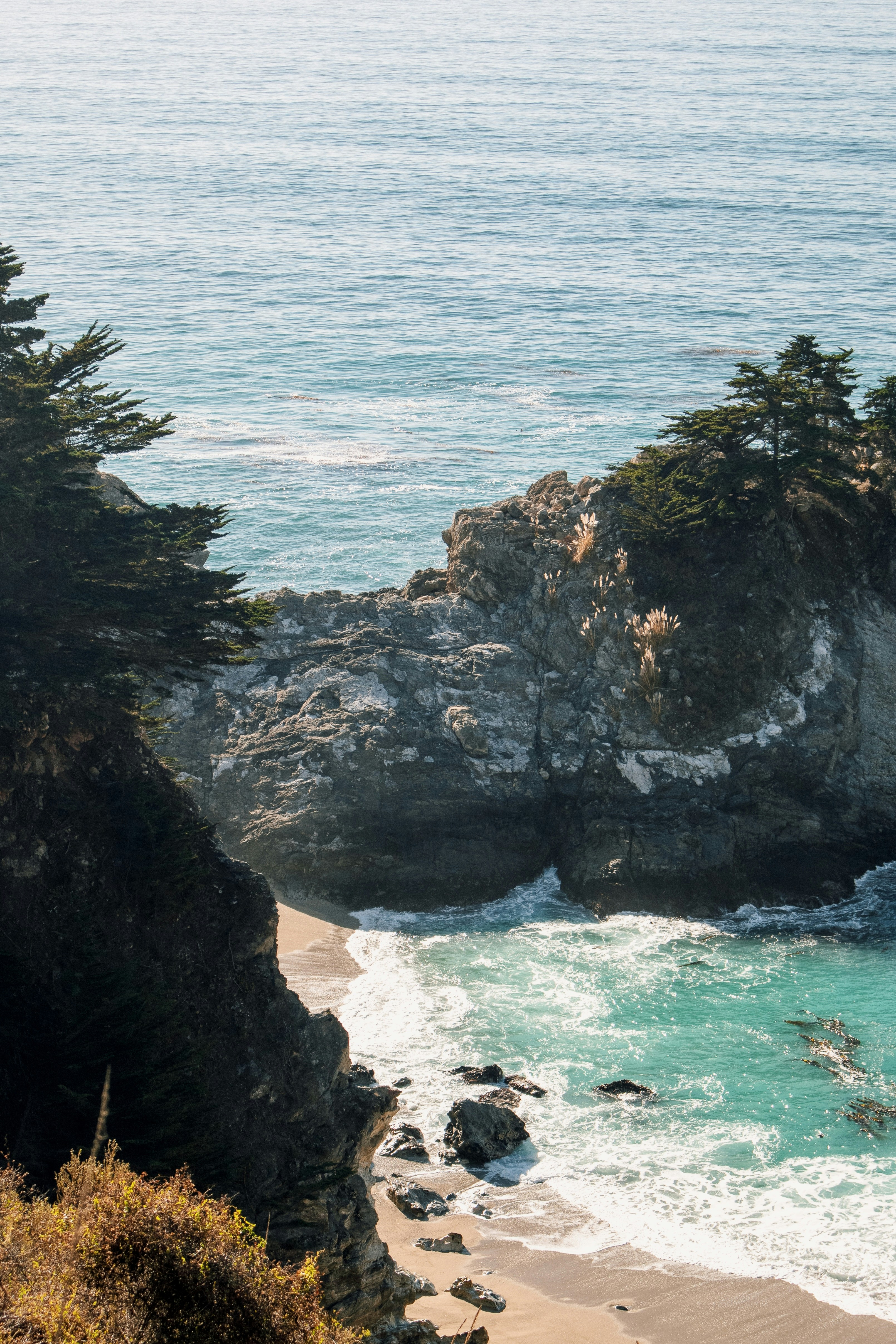 Rocky coastal formation with turquoise waters lapping at the sandy shore, framed by lush greenery. A tranquil scene capturing the essence of nature's beauty.