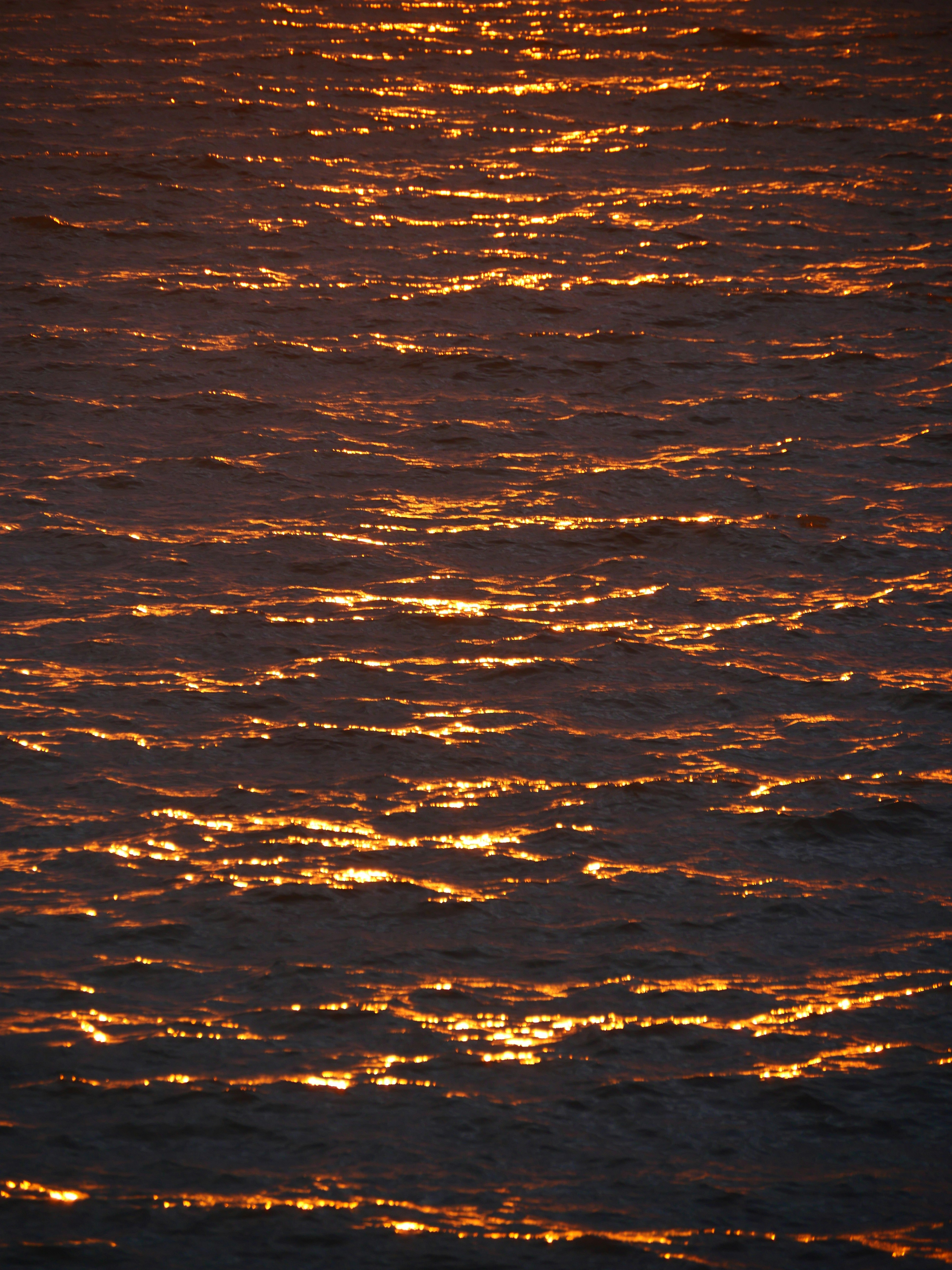 Sunset-lit water fills the frame with warm orange reflections tracing the ripples. Focus remains on the reflective surface and the sea's texture rather than a single subject.