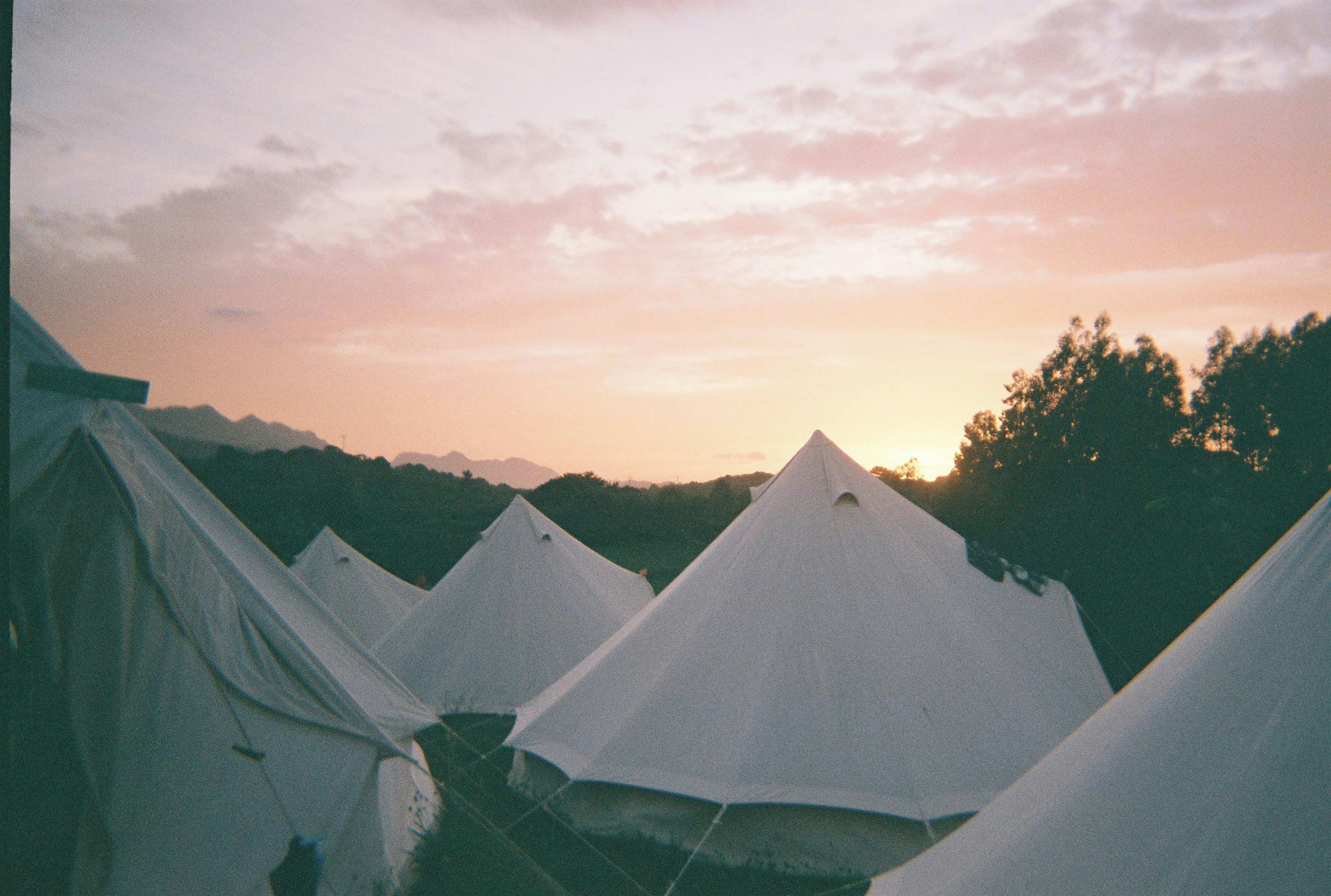 White tents silhouetted against a vibrant sunset, with distant mountains framing the scene.