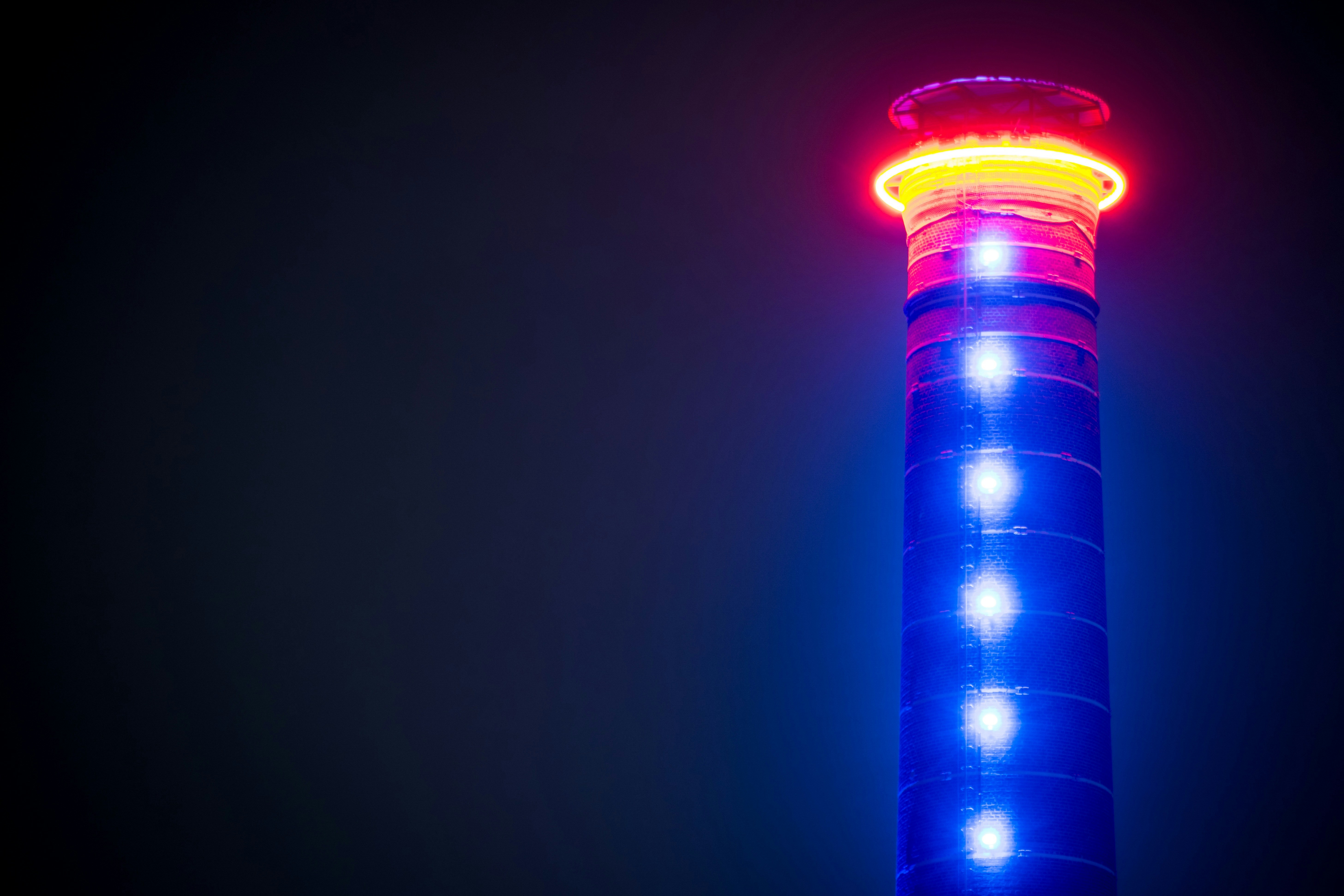Tall tower illuminated with vibrant blue and red lights against a dark sky.