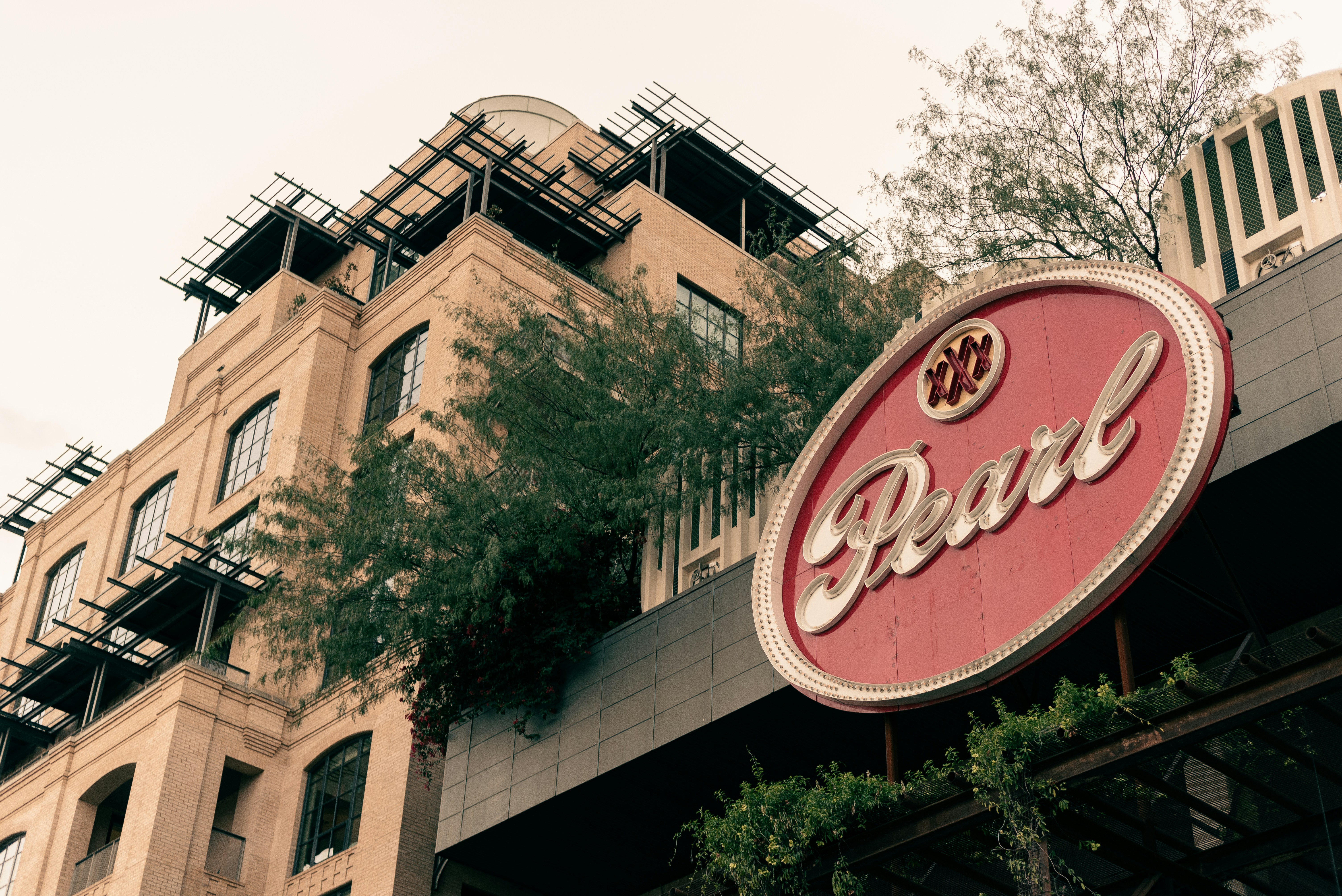 Red circular sign with 'Pearl' logo on a stone building adorned with greenery and metalwork.