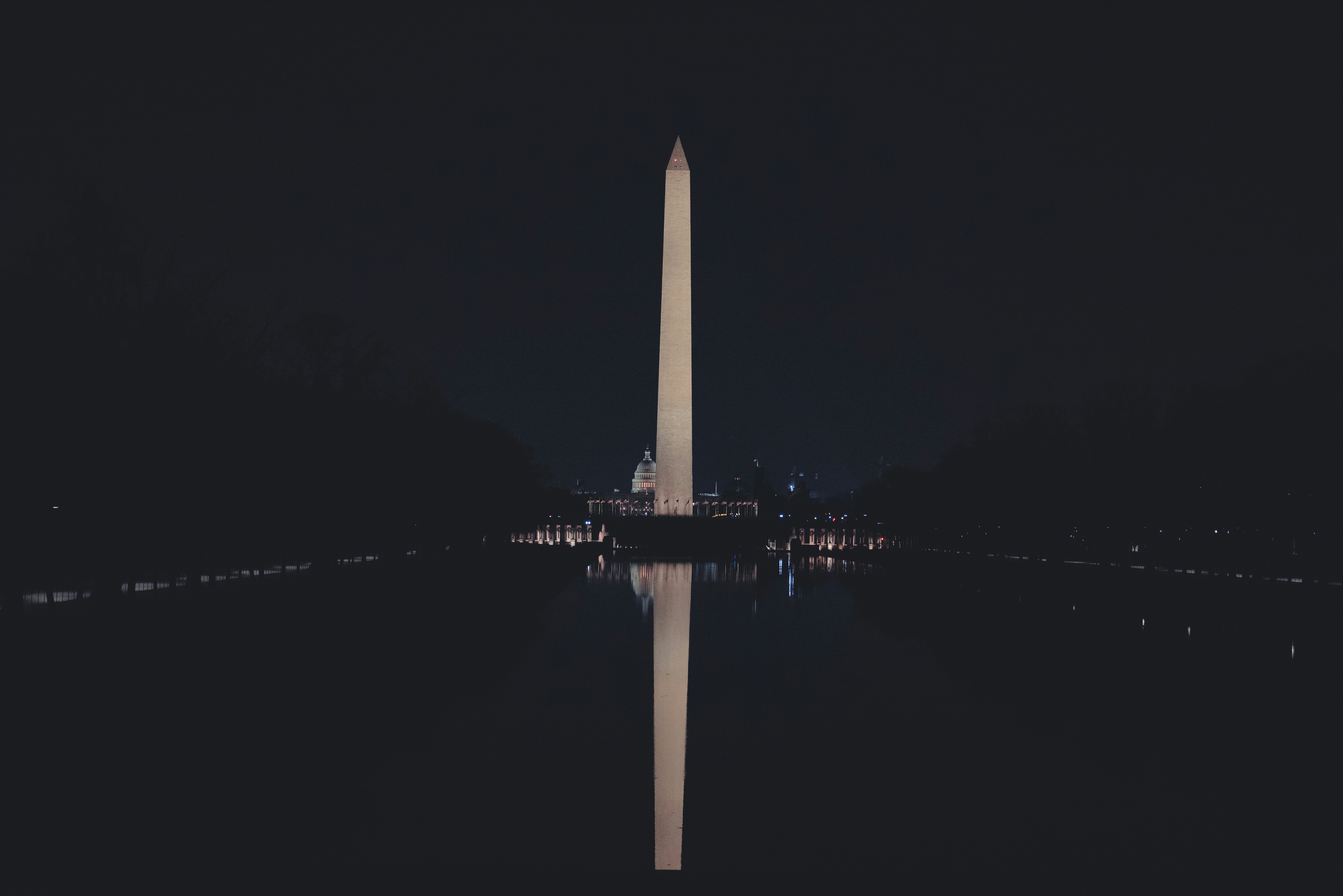 The Washington Monument stands tall against a dark sky, its reflection shimmering in the water below, creating a serene nighttime scene.