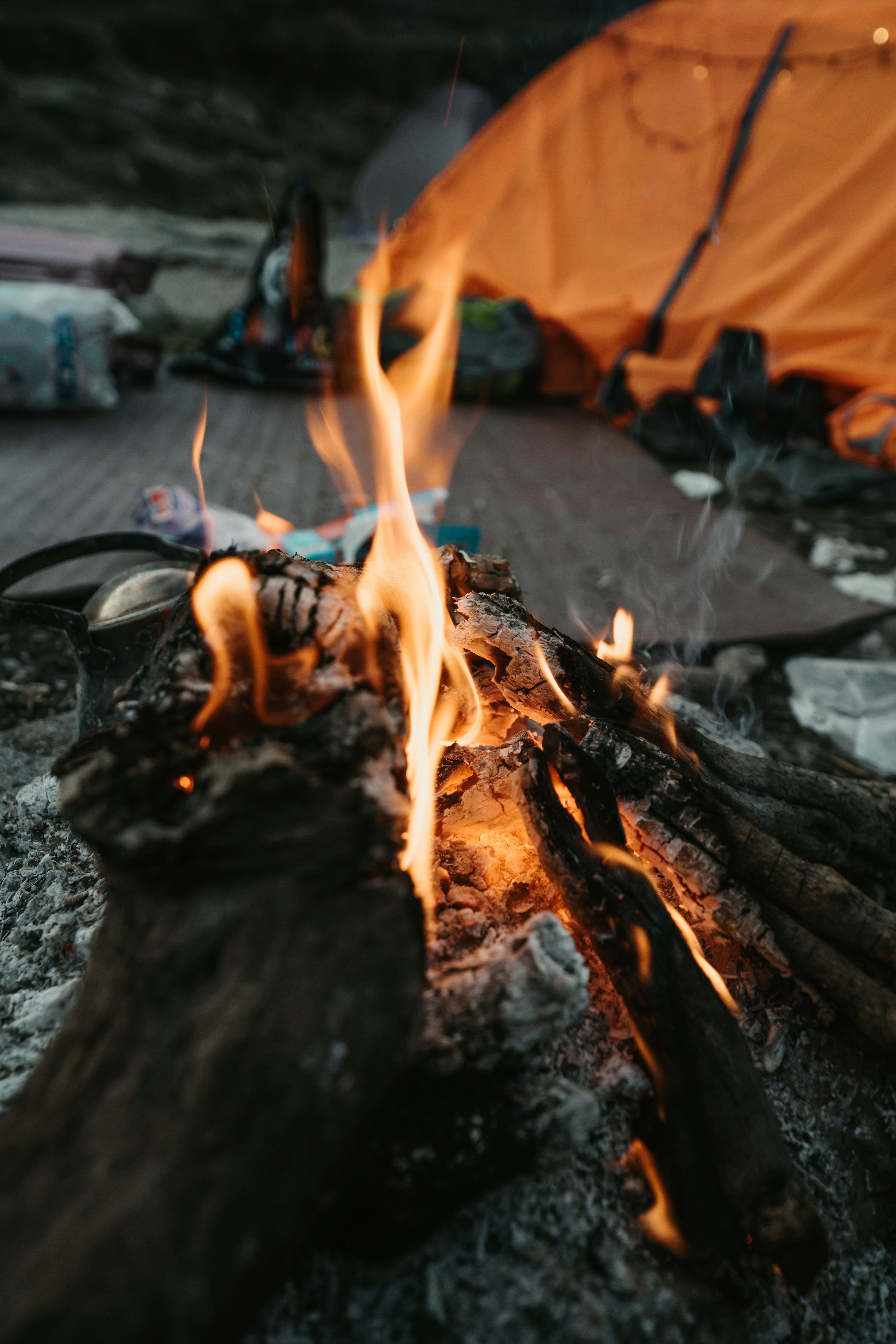Ember Portrait: Campfire Glow Framing Gear and Orange Tent at Dusk