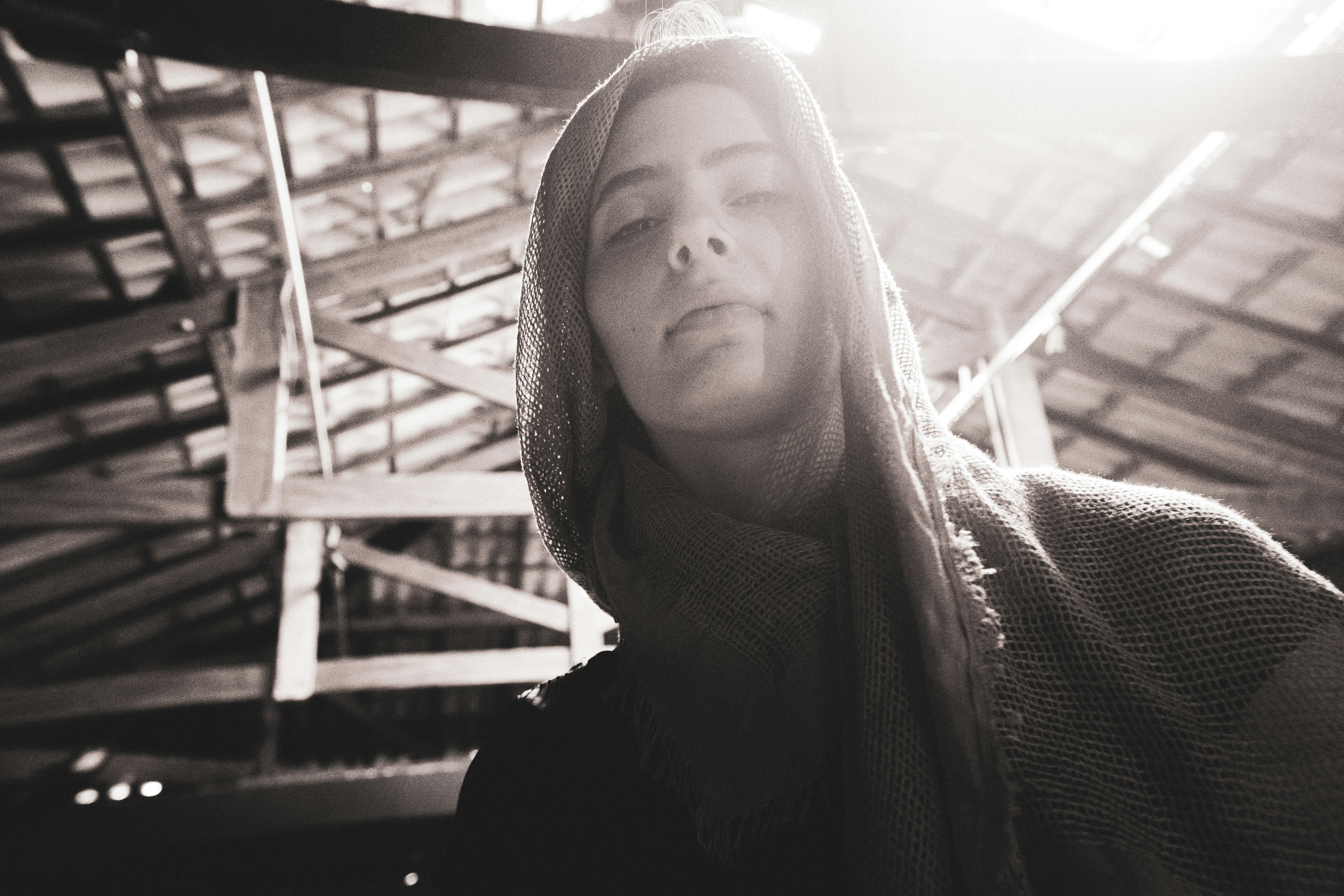 Hooded Gaze Beneath Steel Beams: A Quiet Portrait in Backlit Geometry