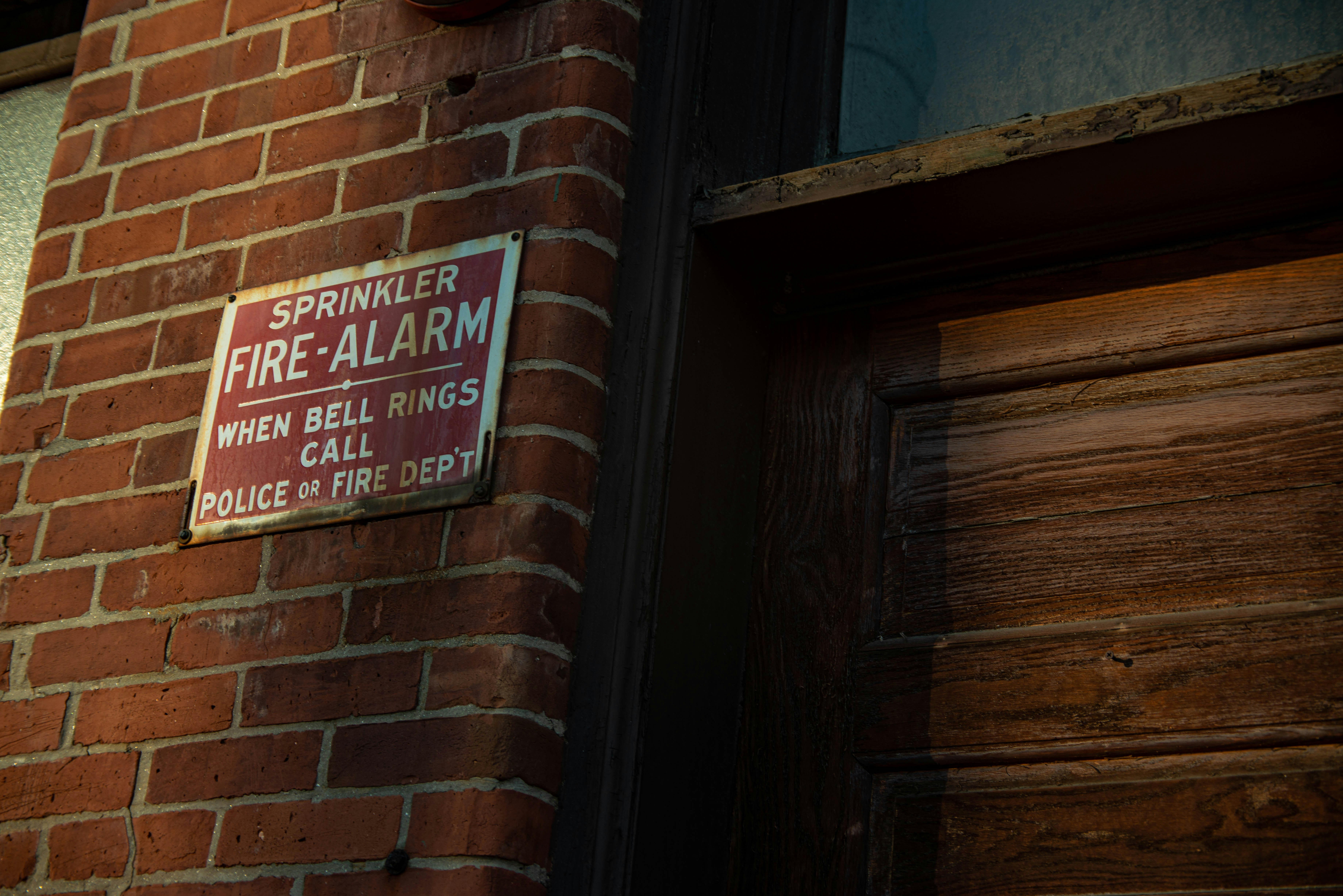 Brick Wall Fire Alarm Sign Near a Wooden Door