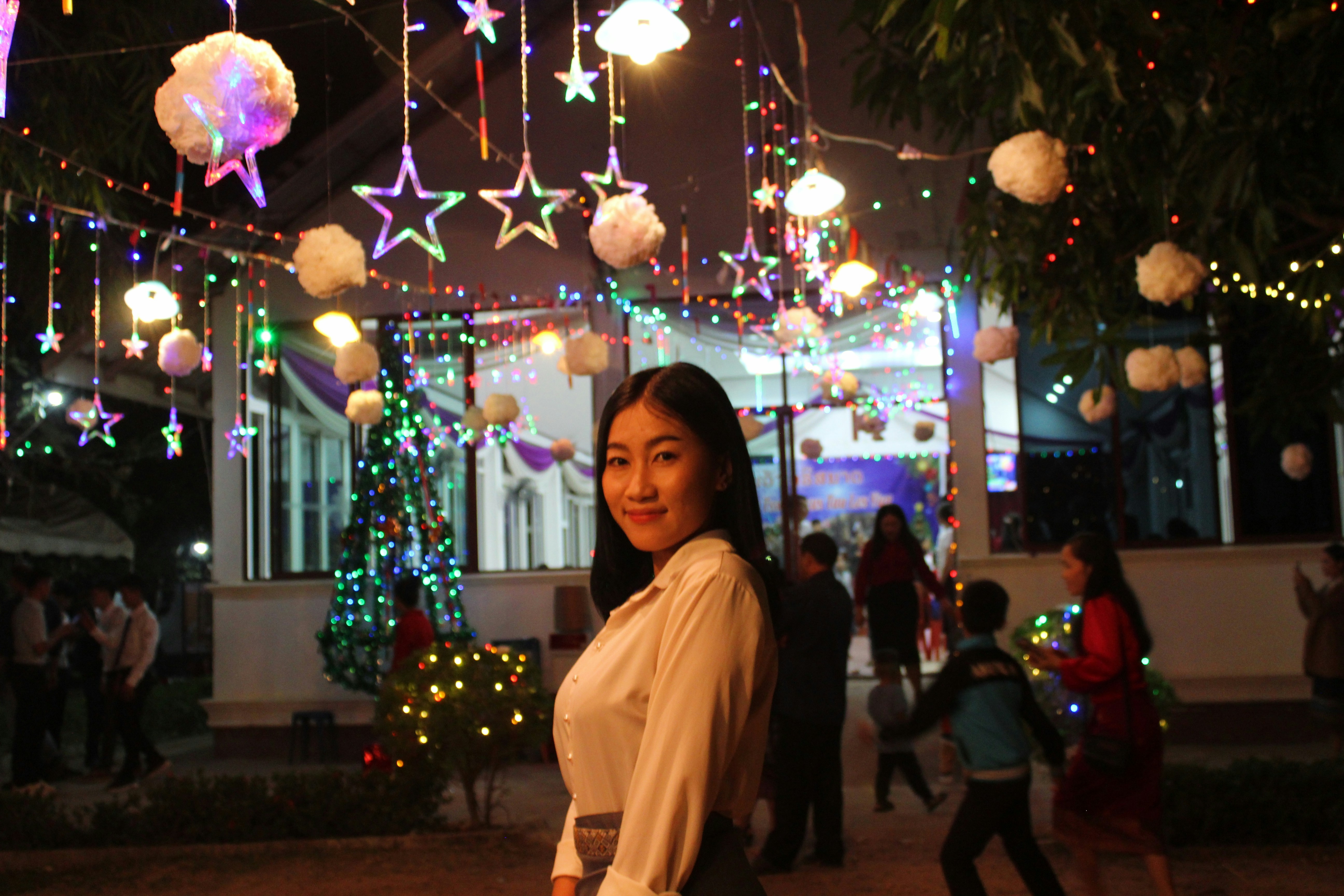 Woman smiling amidst colorful star and cloud decorations at night.