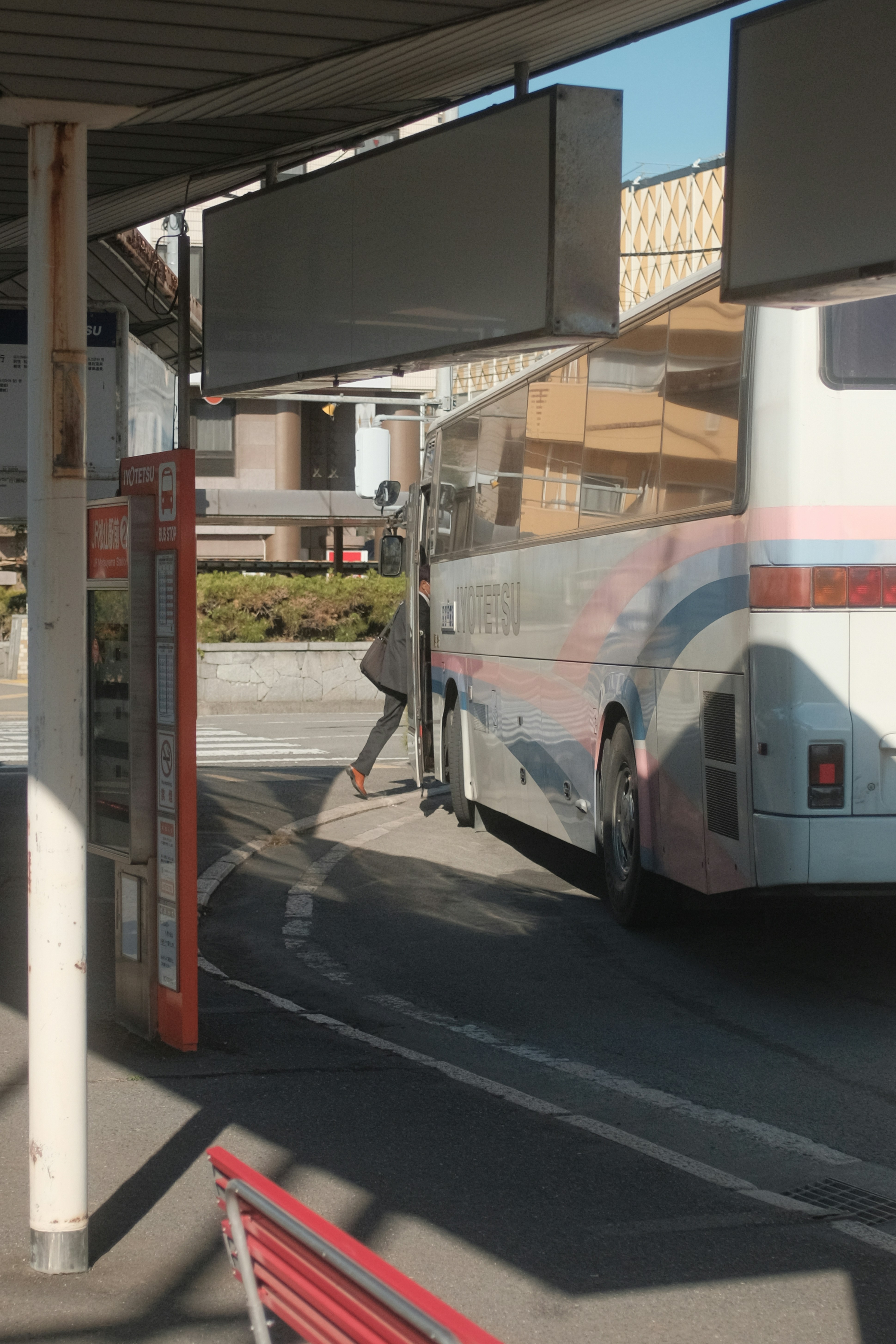 A bus prepares to depart from a station, with a passenger stepping off the curb. The setting captures the essence of travel and transition.