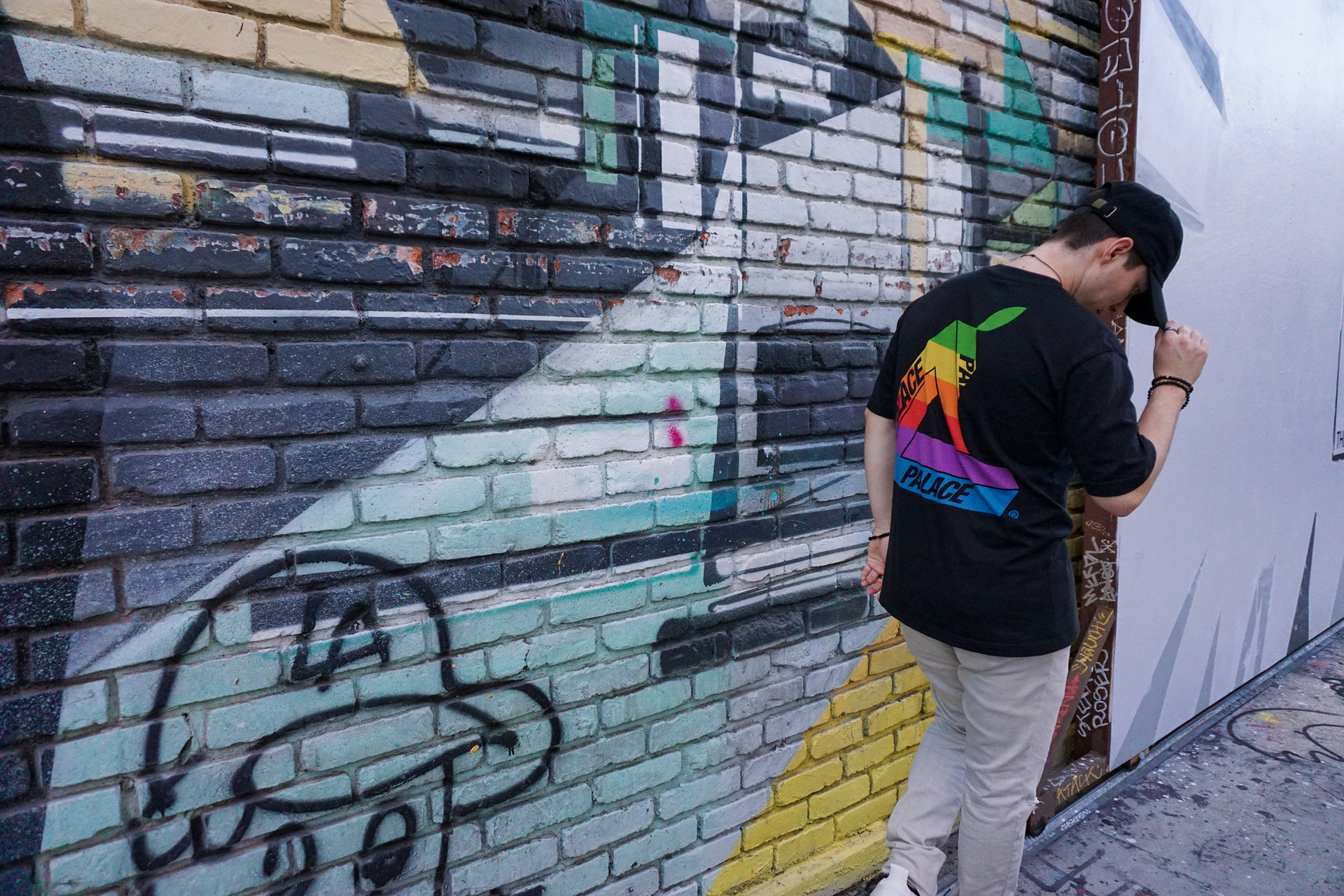 A young person in a colorful shirt stands pensively against a graffiti-covered wall, embodying the spirit of urban art and culture.