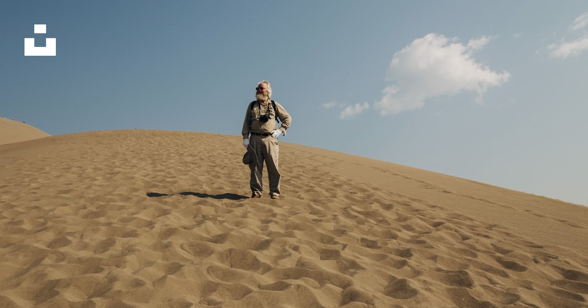 Woman In Brown Jacket And Black Pants Walking On Brown Sand During