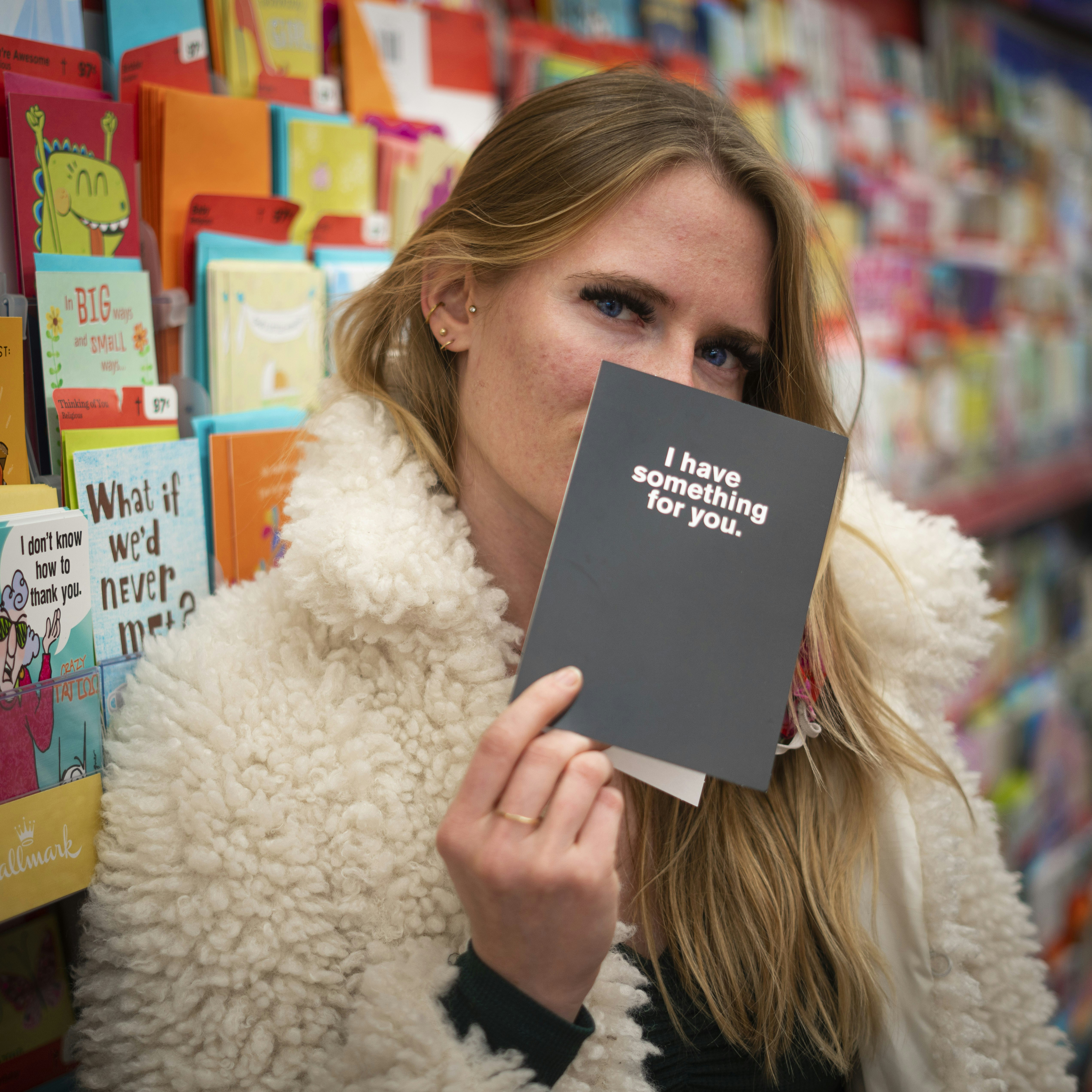 Woman holding a gray card with a message in a vibrant card shop. Surrounding greeting cards add a playful backdrop.