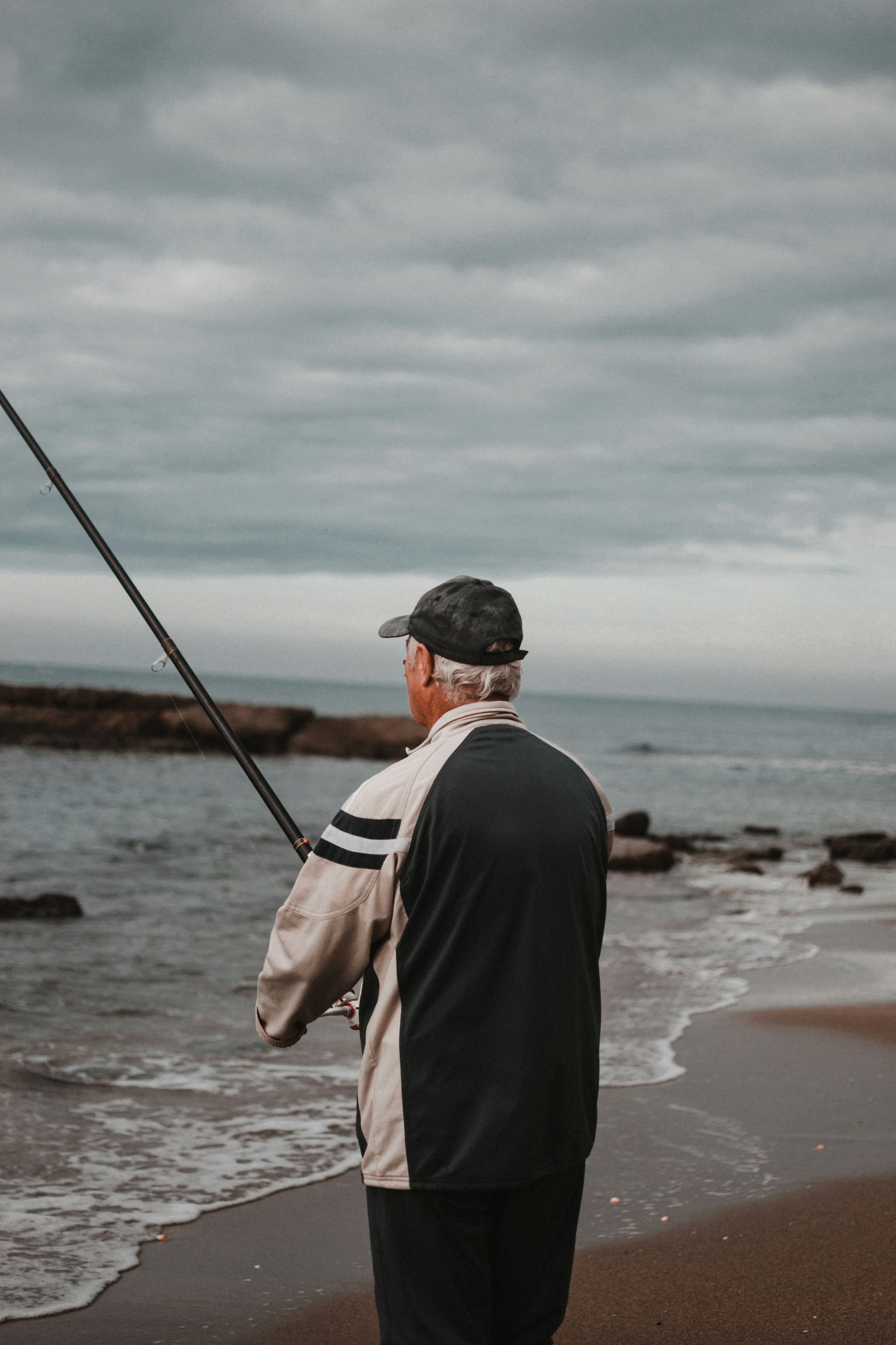 Quiet Shoreline: A Back-Turned Fisherman Stares Toward the Moody Sea