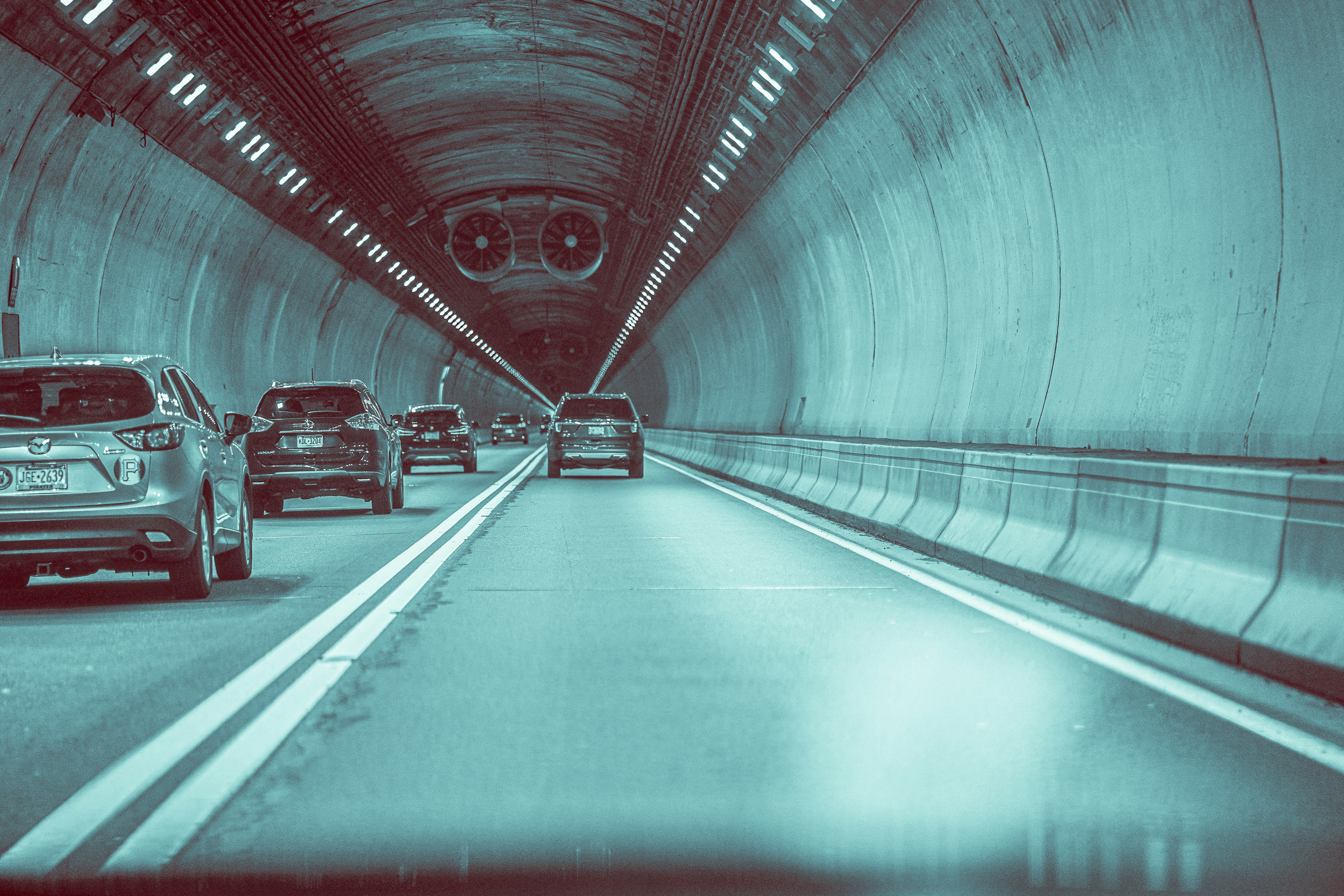Cars driving through a dimly lit tunnel with reflections casting a bluish hue.
