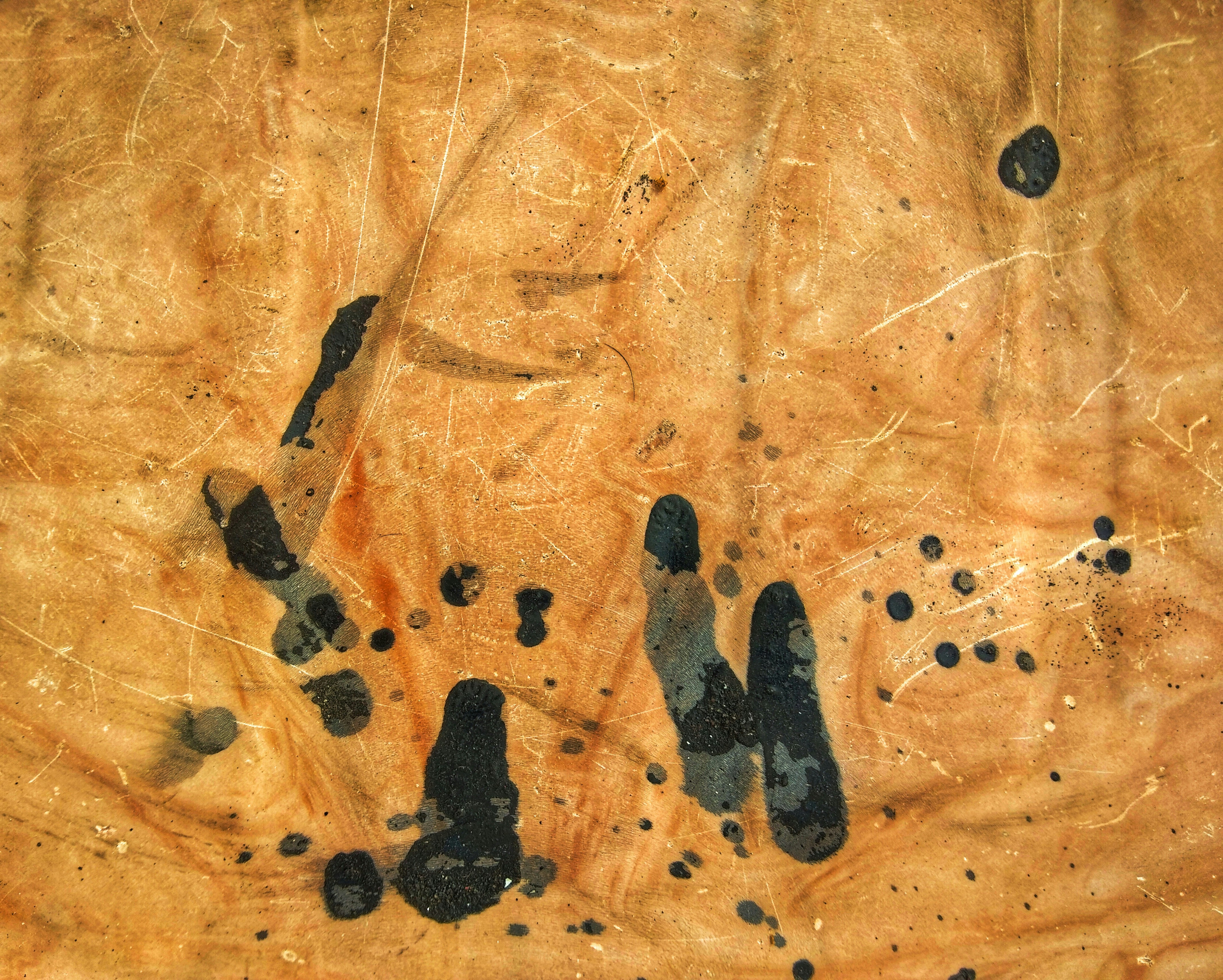 Textured surface with dark paint splatters and scratches on a warm, earthy background.
