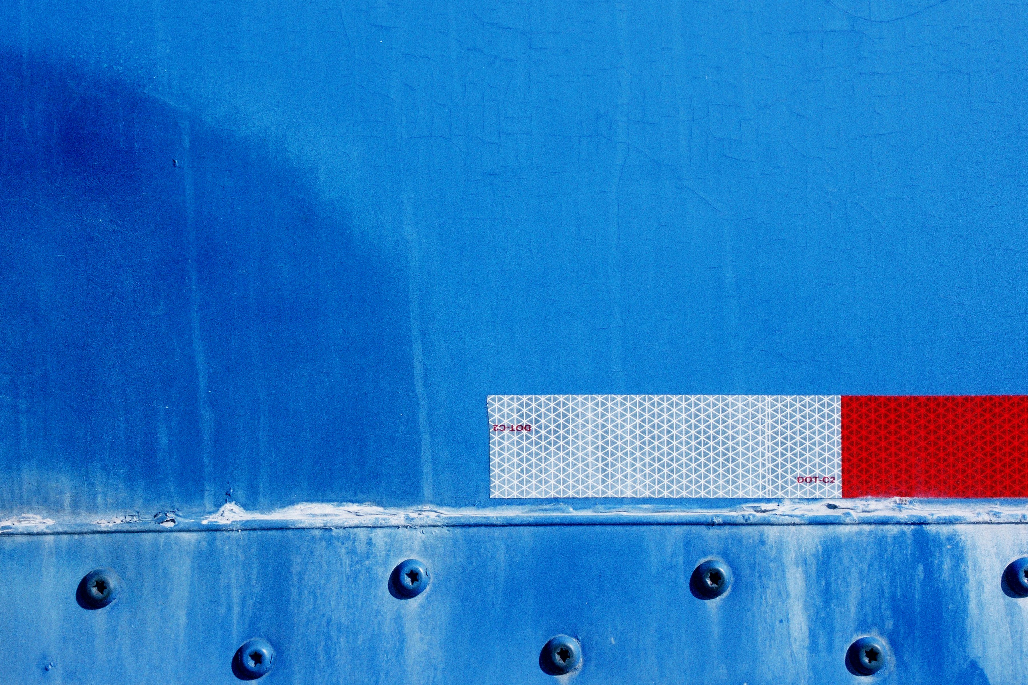Abstract composition of a blue metal surface featuring reflective red and white markings. The image highlights the interplay of color and texture.