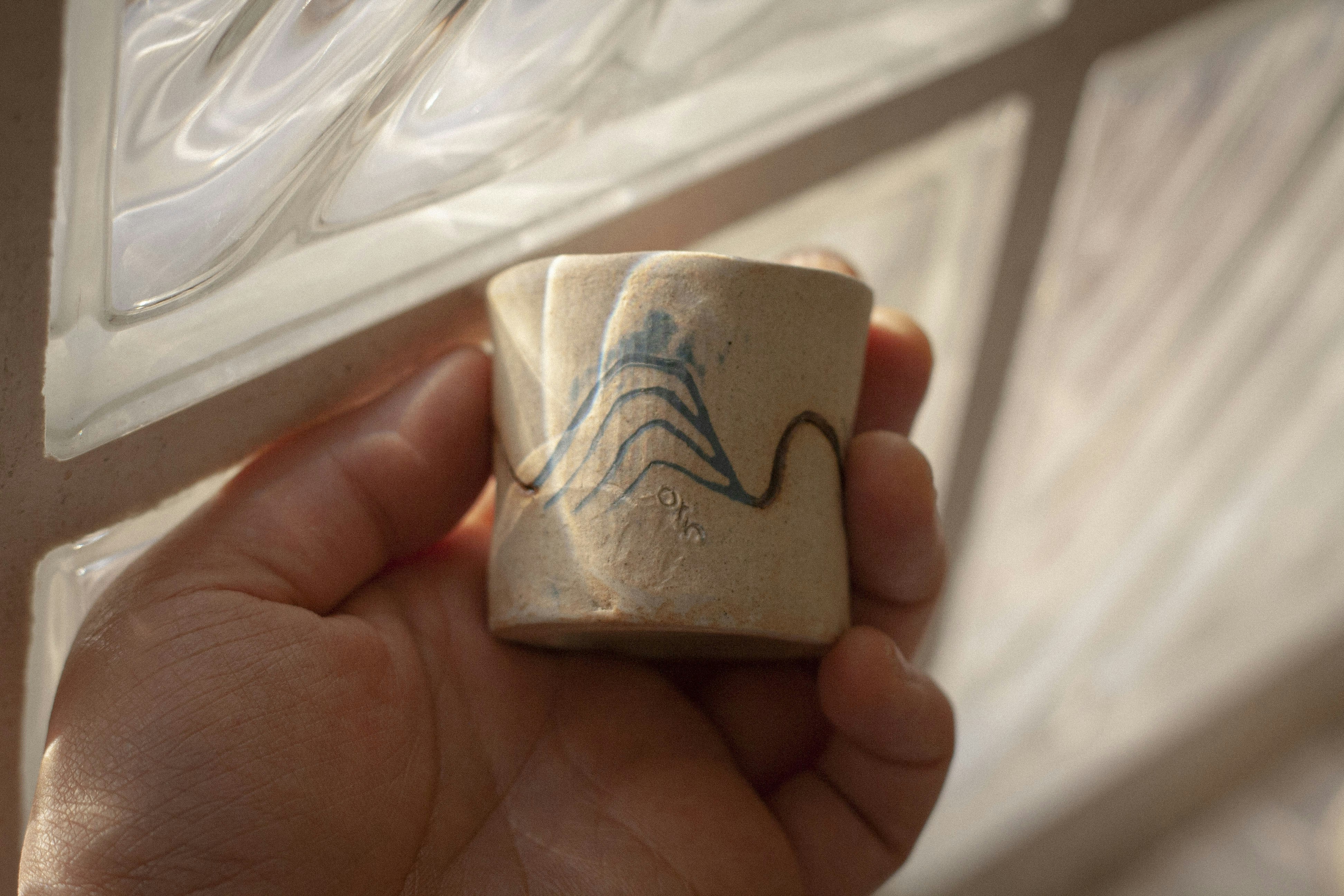 Hand holding a beautifully crafted pottery piece adorned with a delicate wave design. The soft light highlights its texture and artistry.