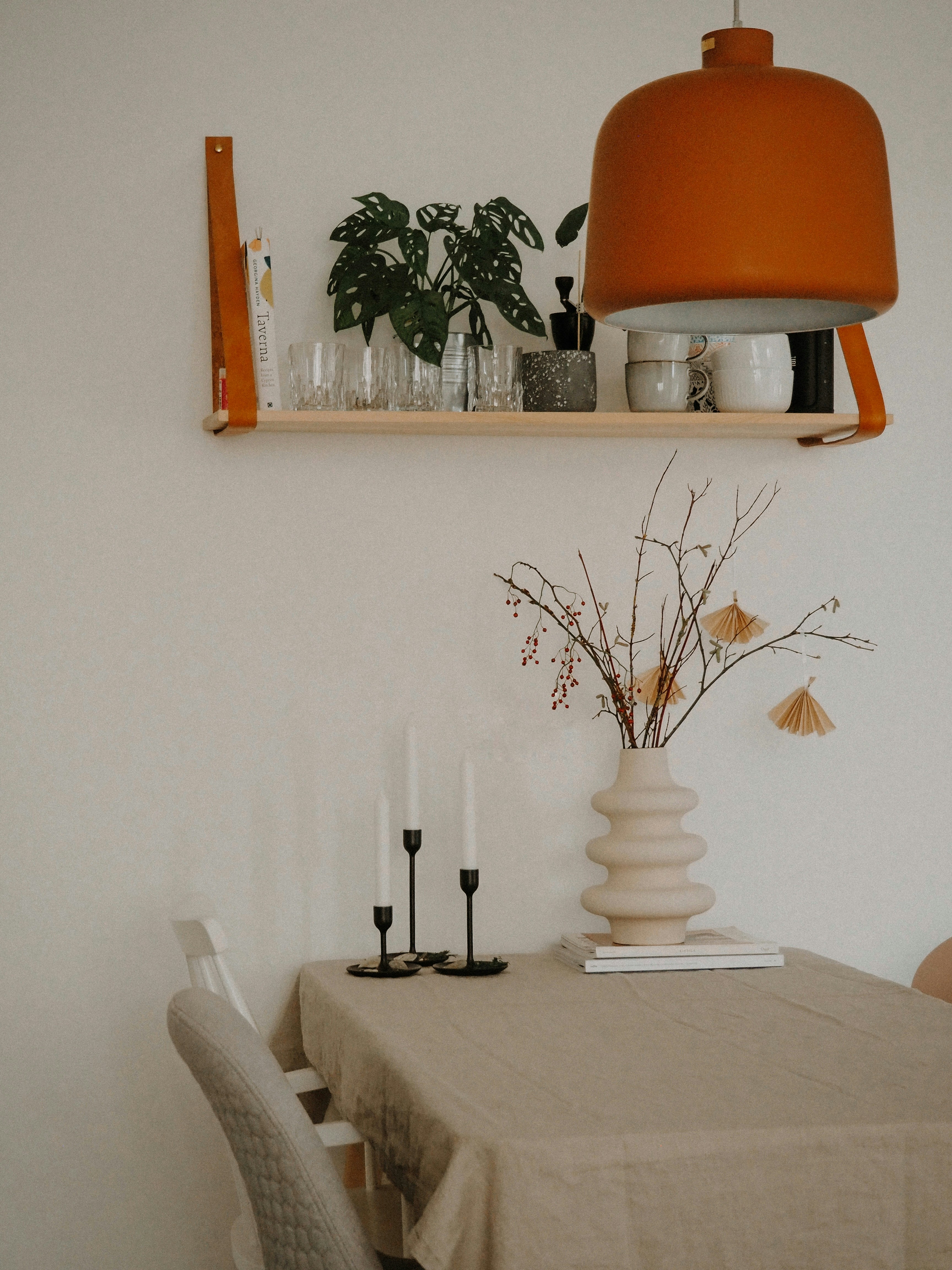 Minimalist dining area with a beige tablecloth, sculptural vase, and overhead terracotta lamp.