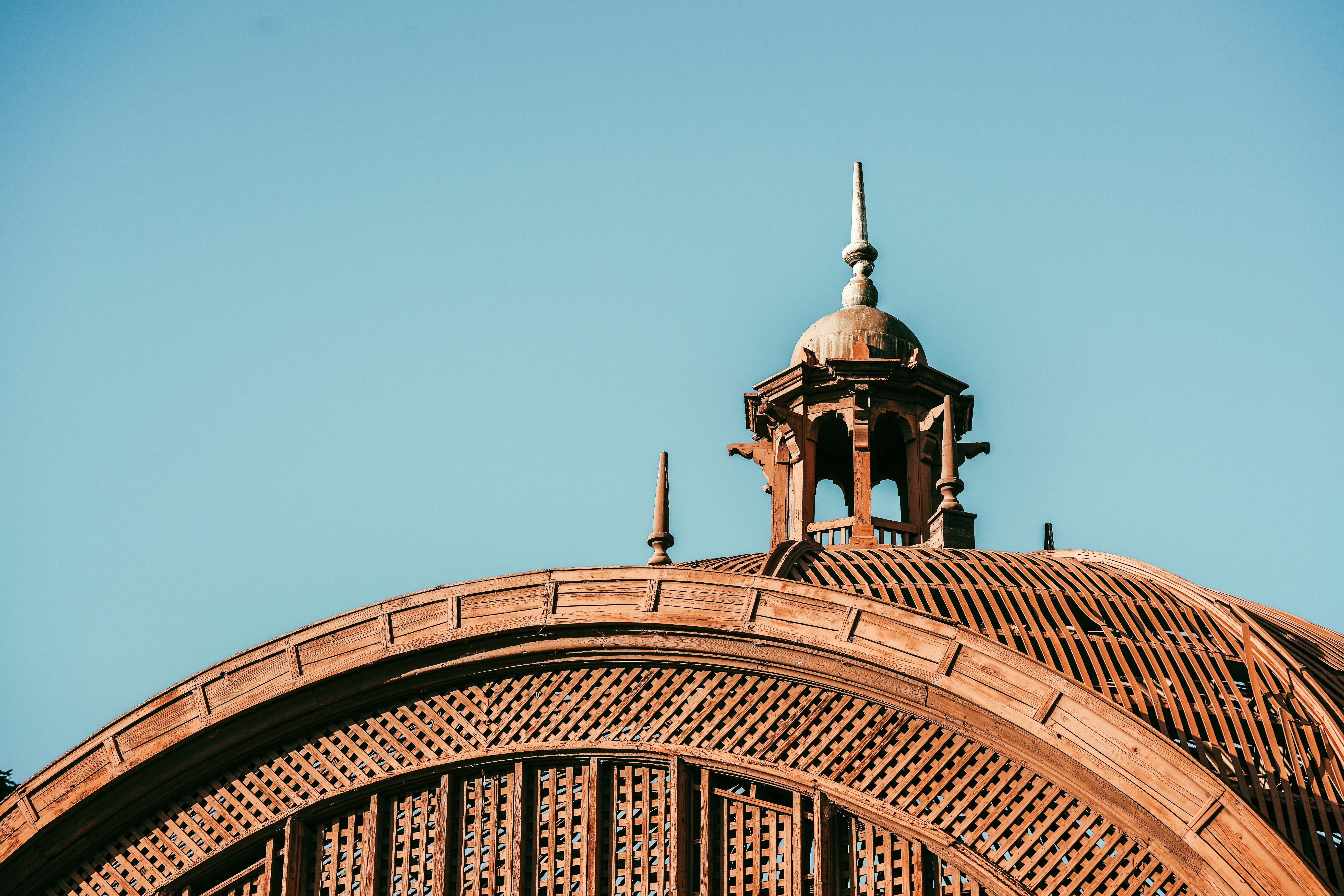 Intricate wooden arch with a decorative spire against a clear blue sky.