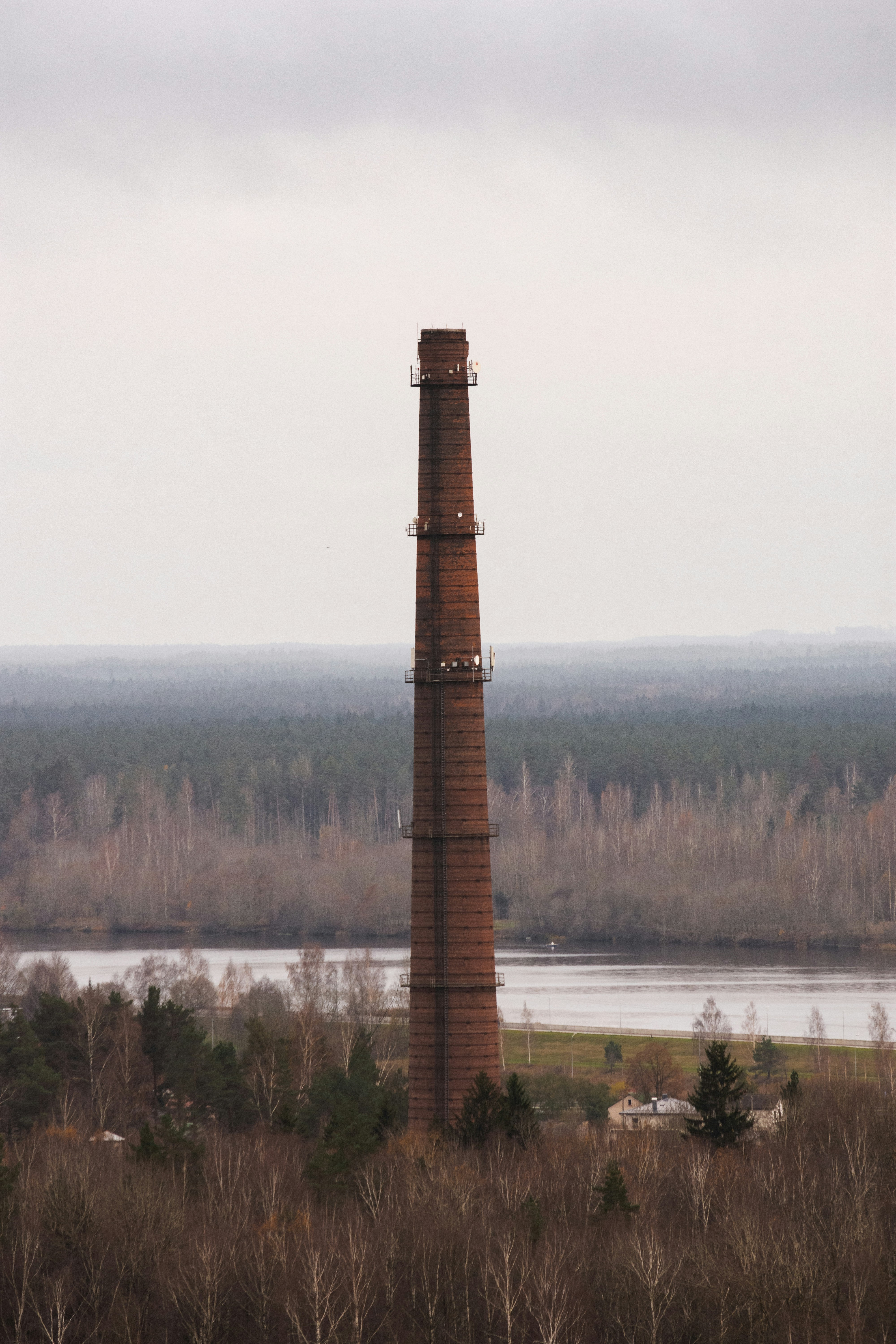 Rusting smokestack rising above a tranquil river, surrounded by a forested landscape.