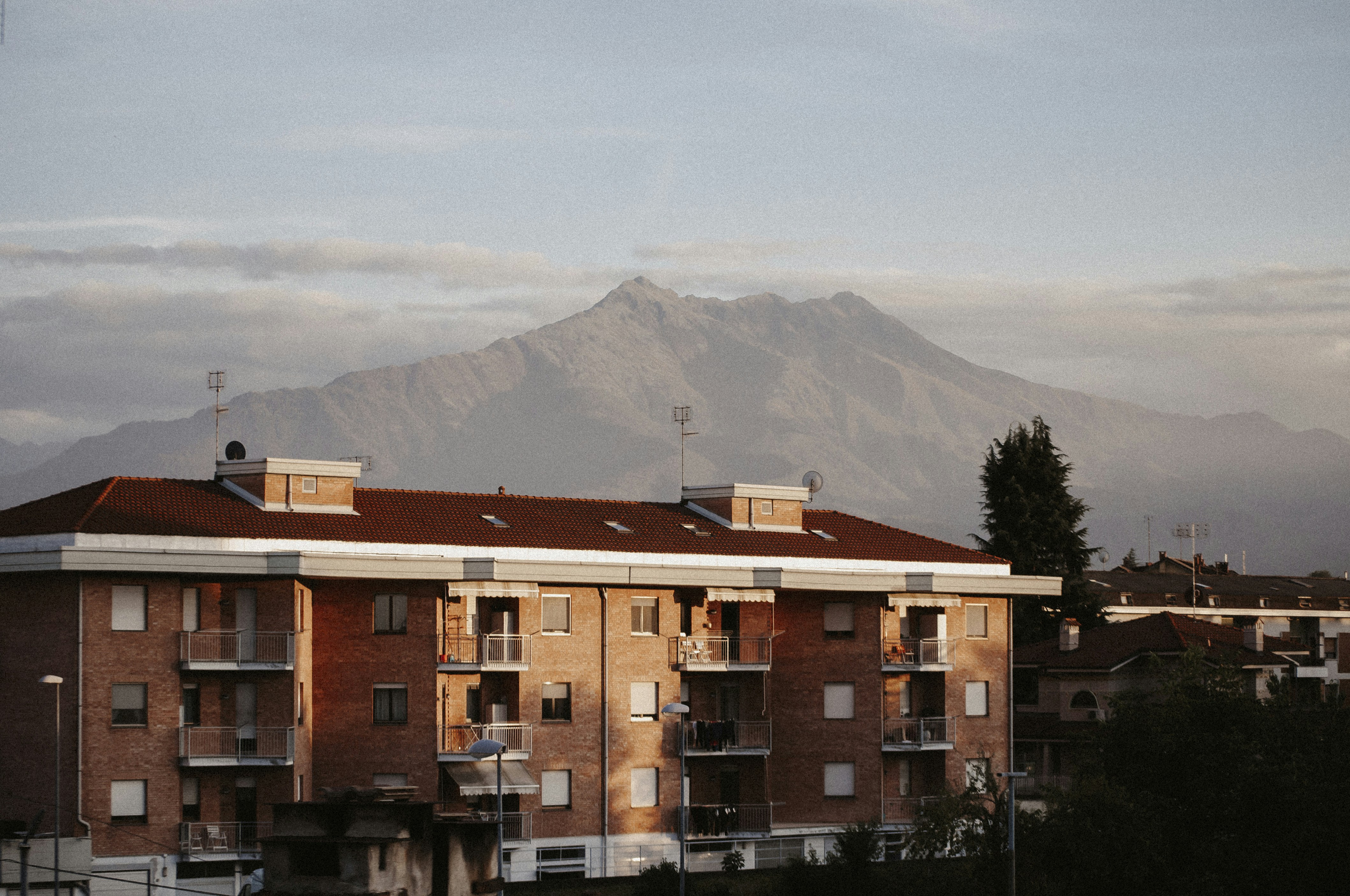 Sunlit apartment building in foreground with a majestic mountain backdrop under a soft sky.