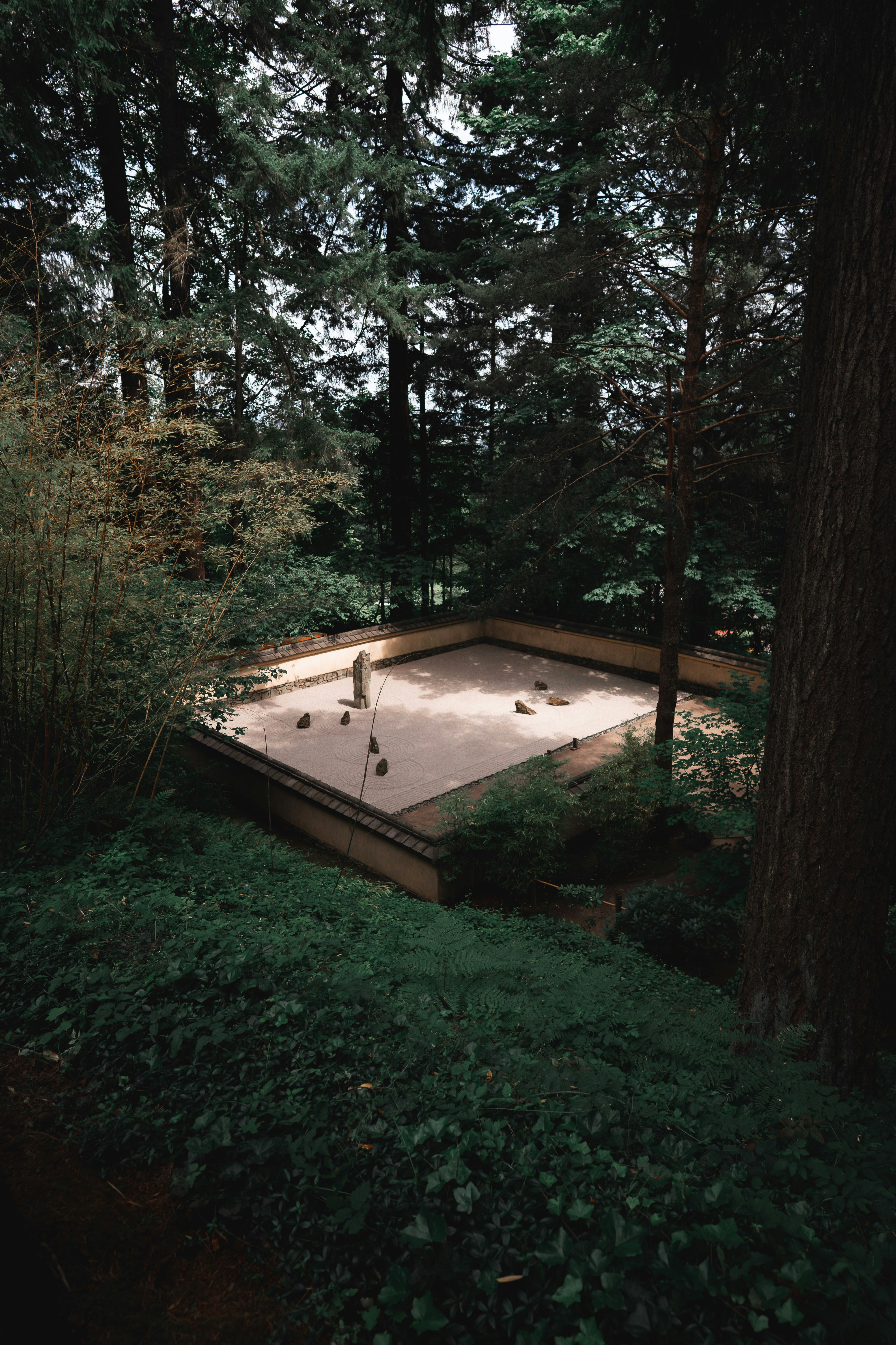 A serene zen garden surrounded by lush greenery, featuring a central stone sculpture and carefully arranged rocks on a sandy surface.
