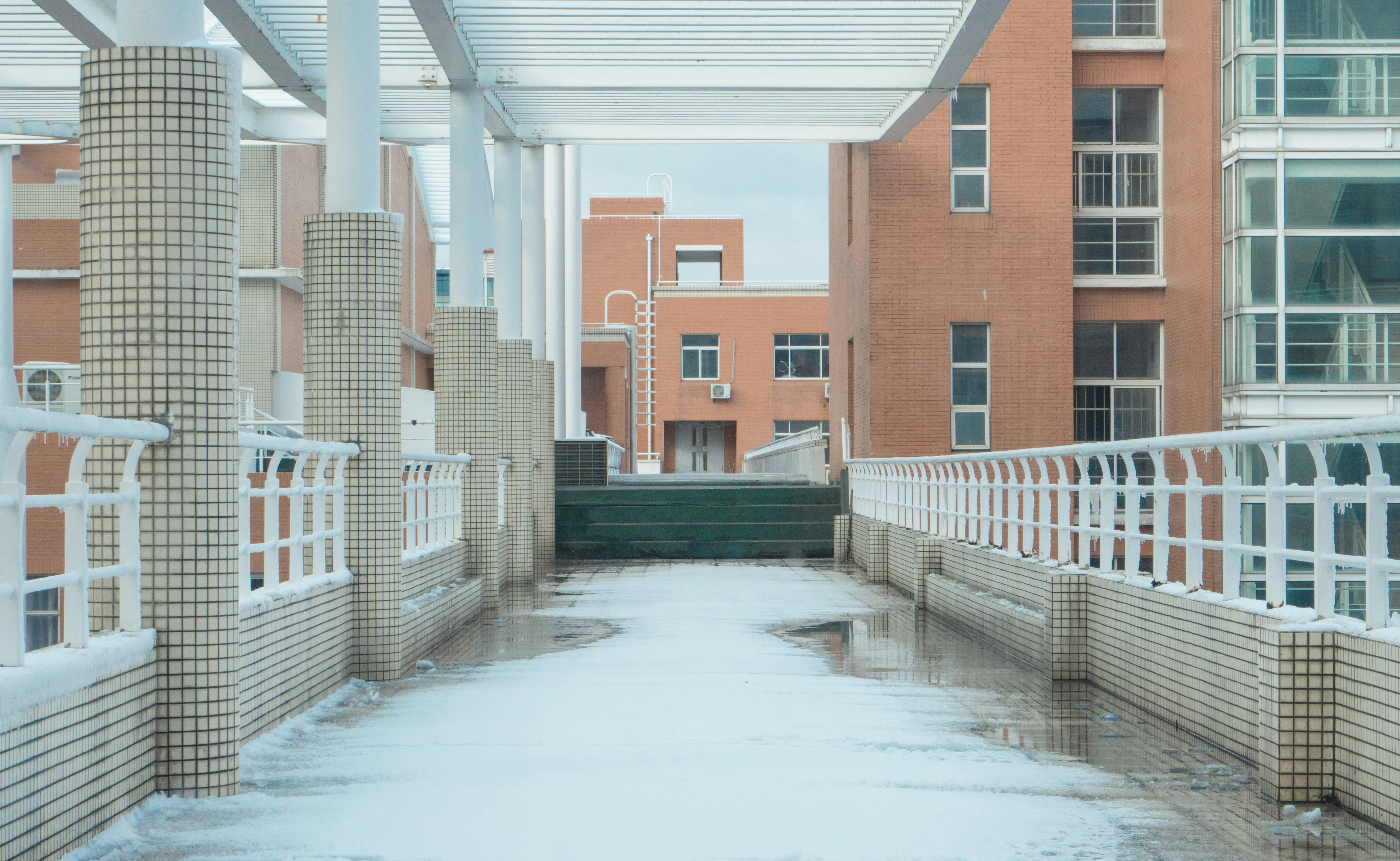 Snow-Capped Skywalk Framing a Distant Green Door in an Urban Campus