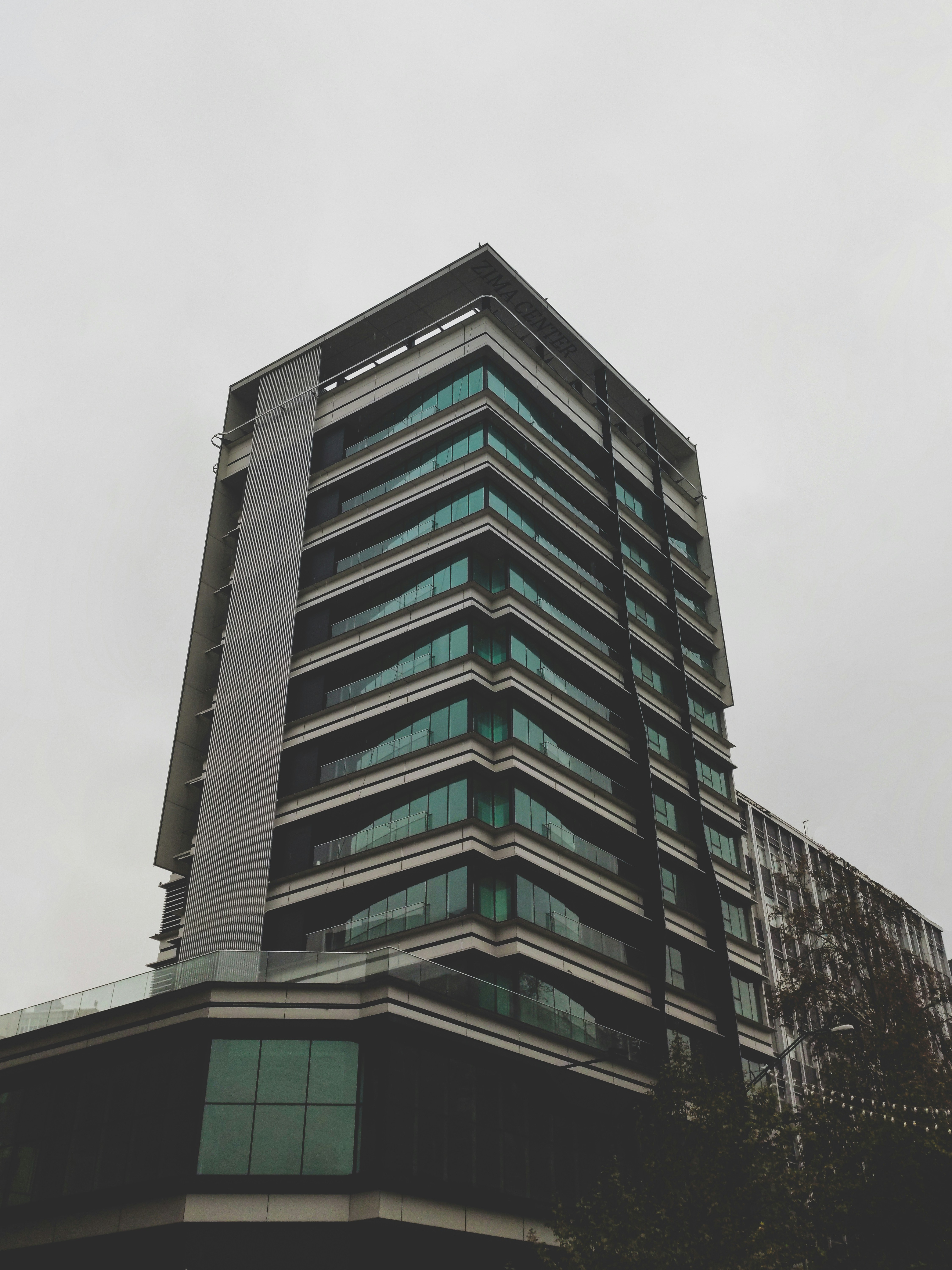Tall modern office tower with stacked glass balconies rises against an overcast sky.
